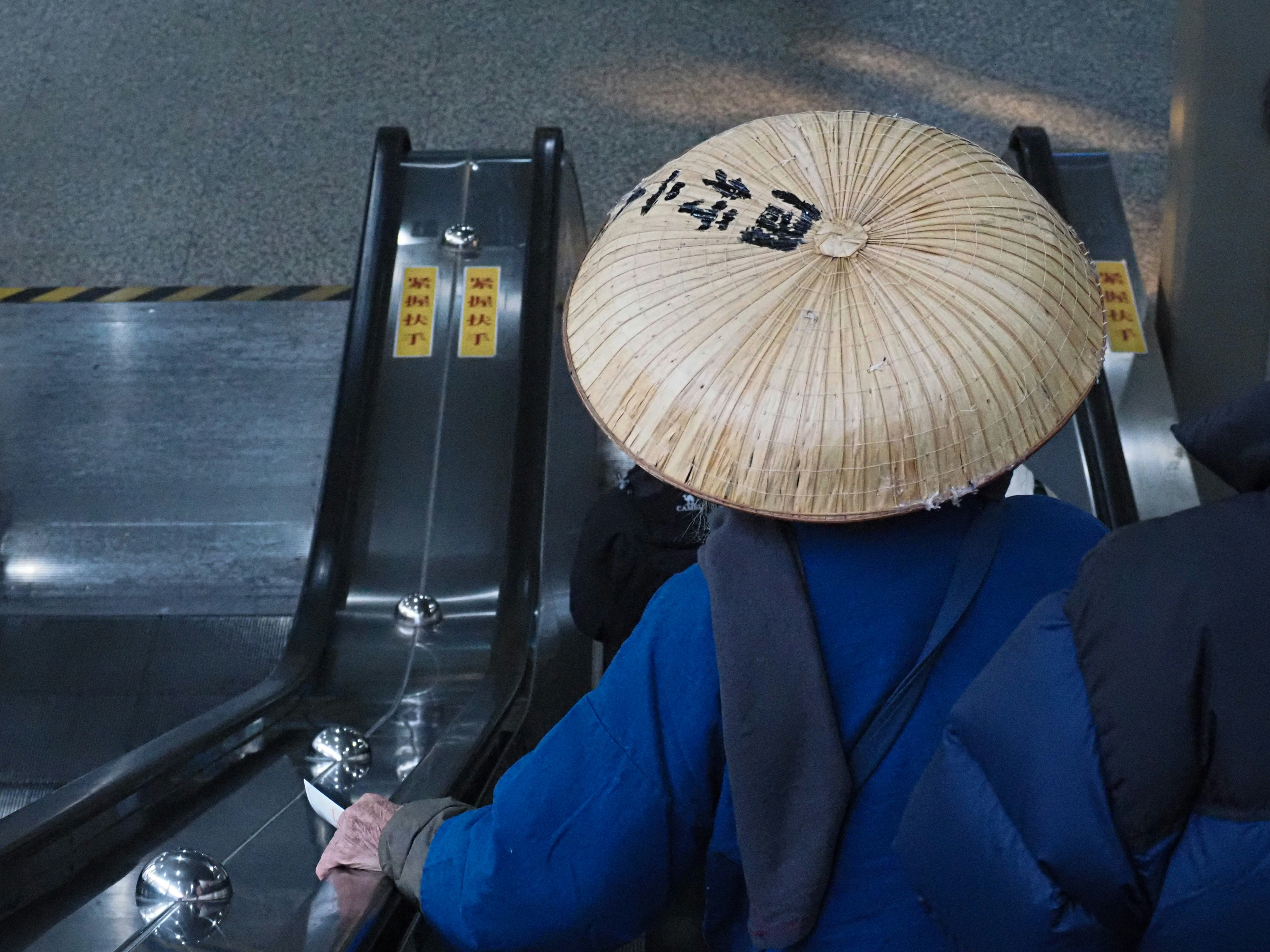 Person wearing a conical hat on an escalator
