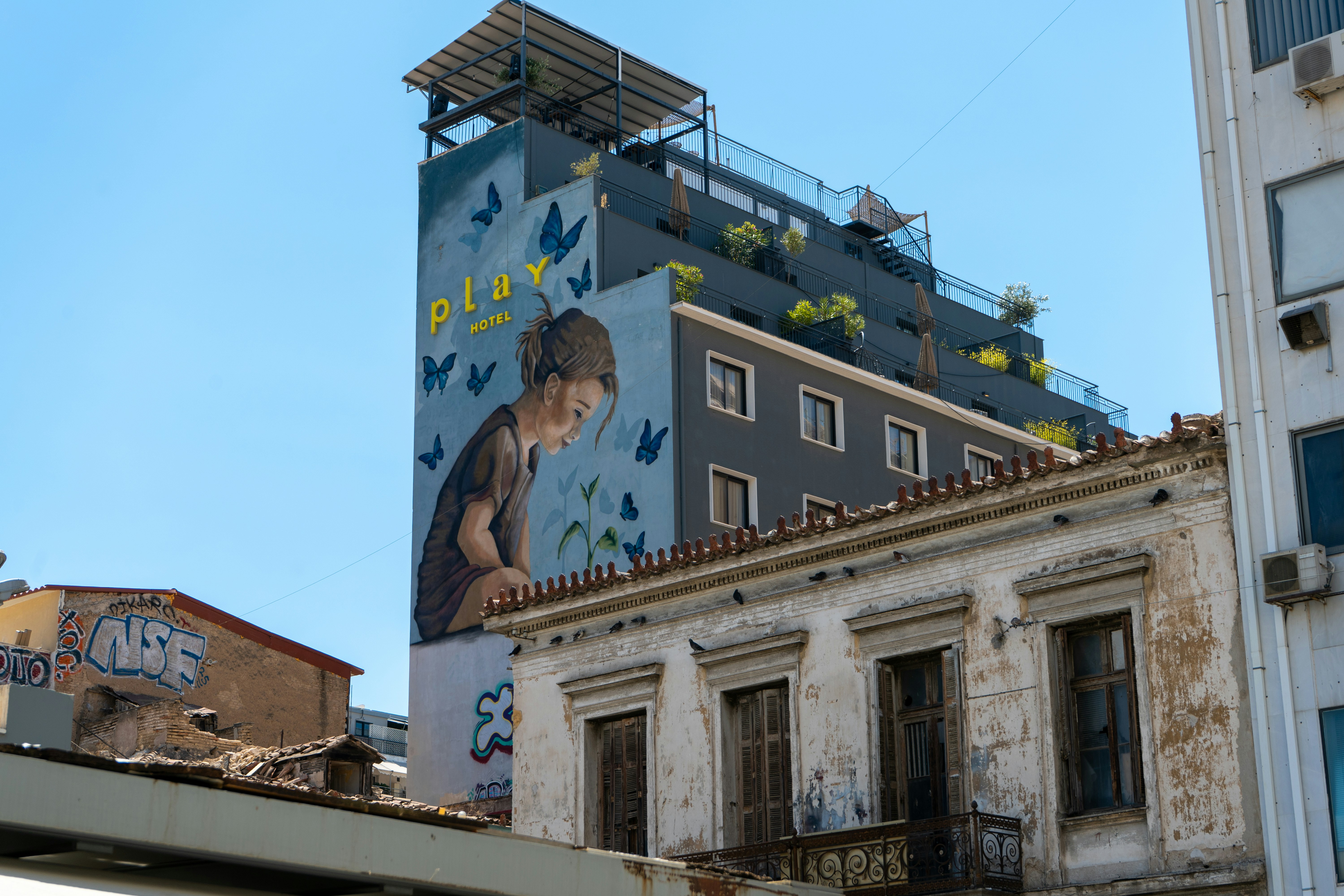 Blue butterfly mural with a rooftop garden tower rising above a worn facade