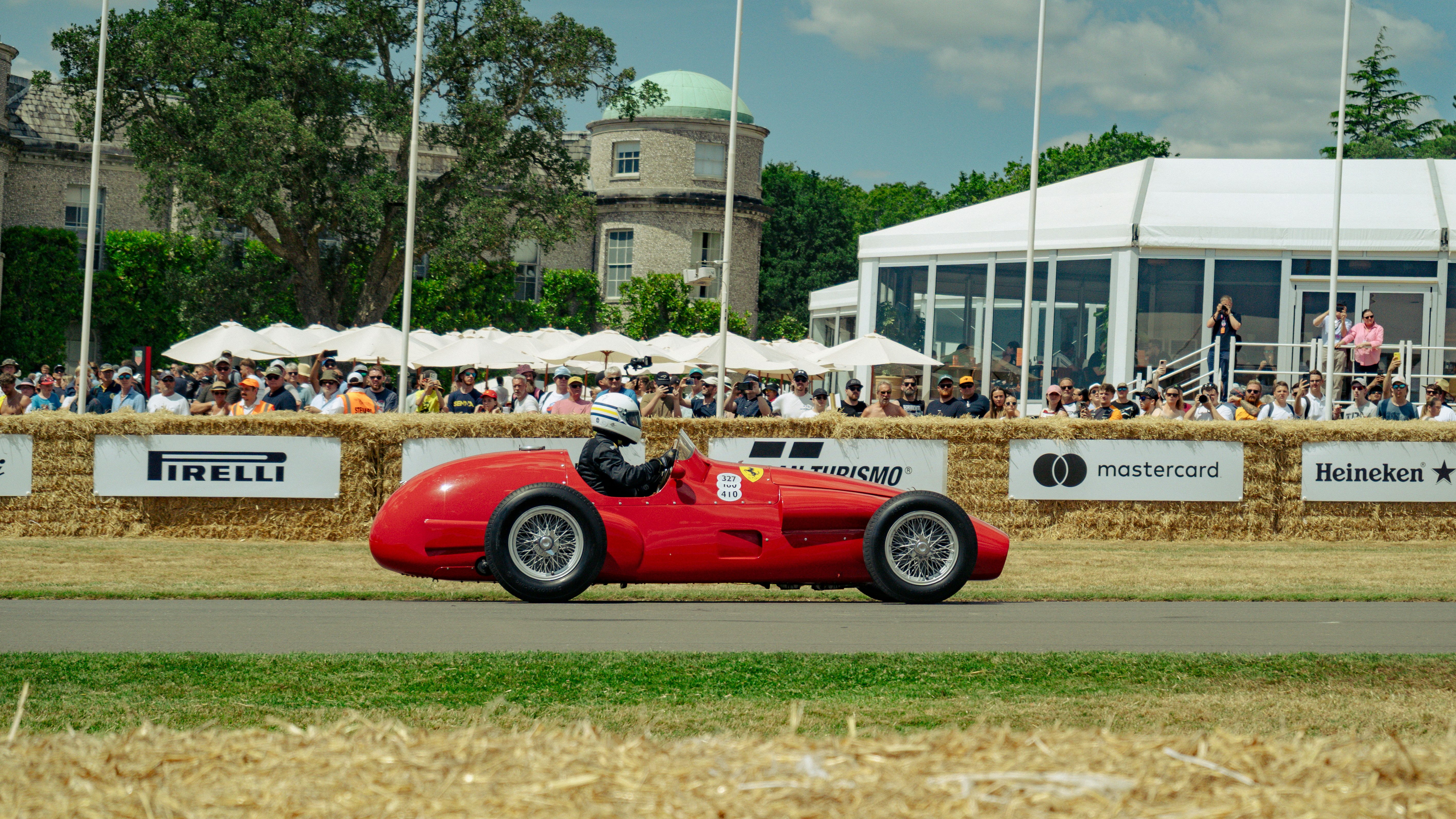 A classic Ferrari Formula 1 car driving along the Goodwood hillclimb during the Goodwood Festival of Speed 2025, with spectators and historic architecture framing the iconic motorsport scene.