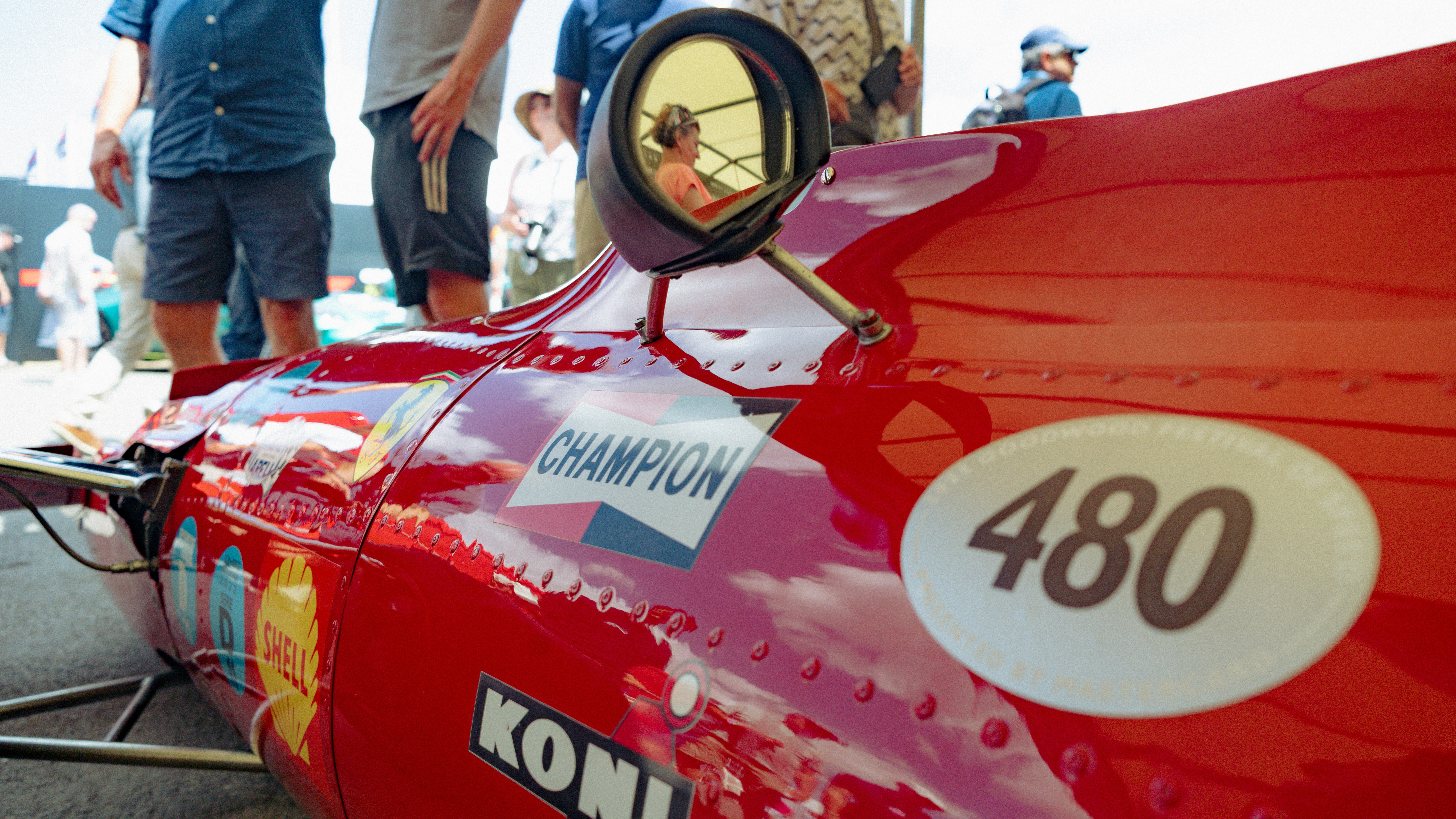 Glossy red racecar with sponsor decals and a prominent number plate, captured at close range near the cockpit area.