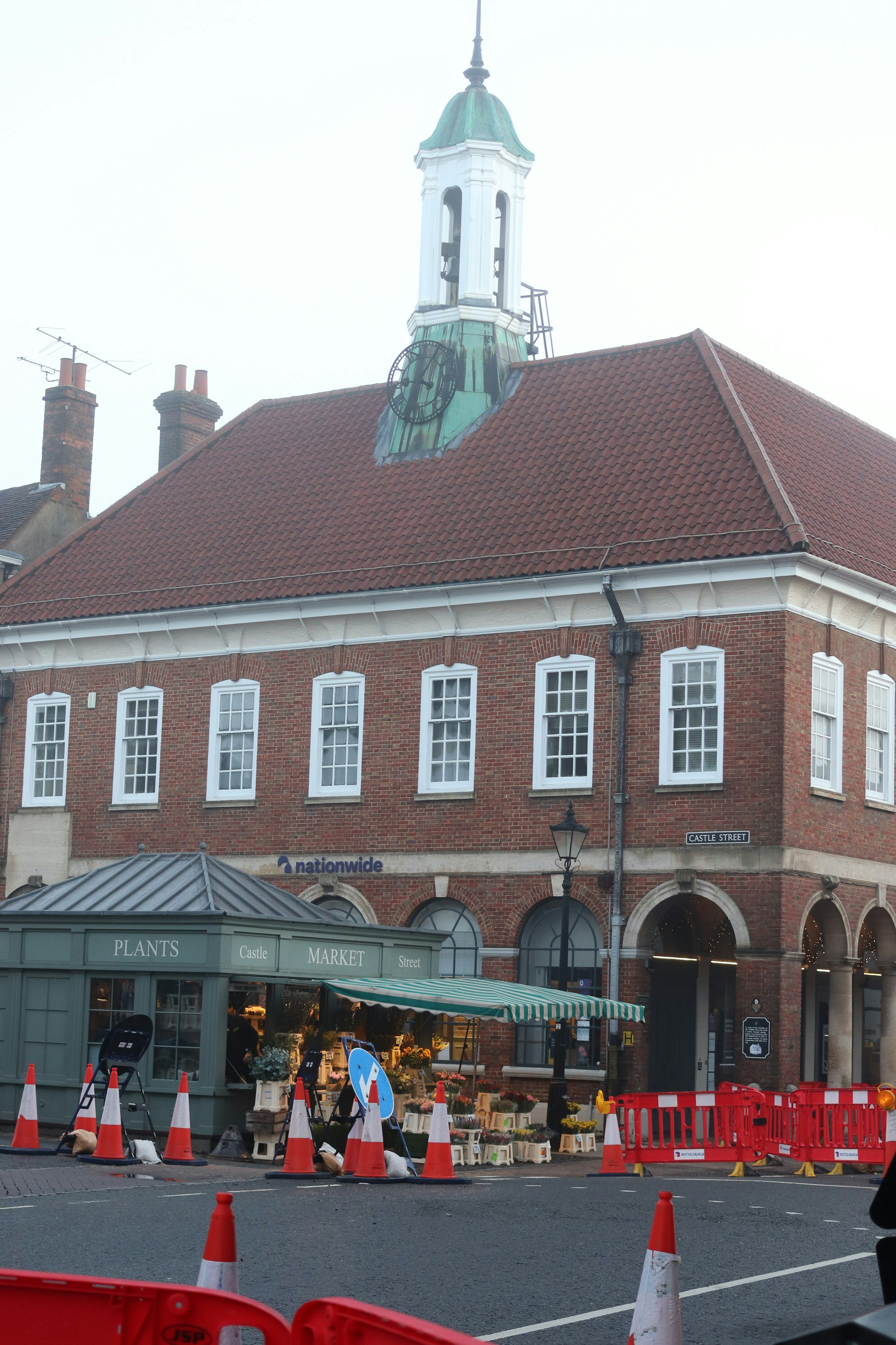Market Cornerstone: Brick Facade, Green Clock Tower, and Street Cones