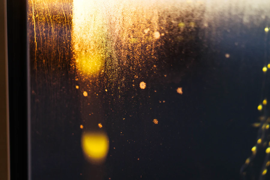Blurry glass with warm city lights and bokeh specks seen through a window at night; abstract urban texture.