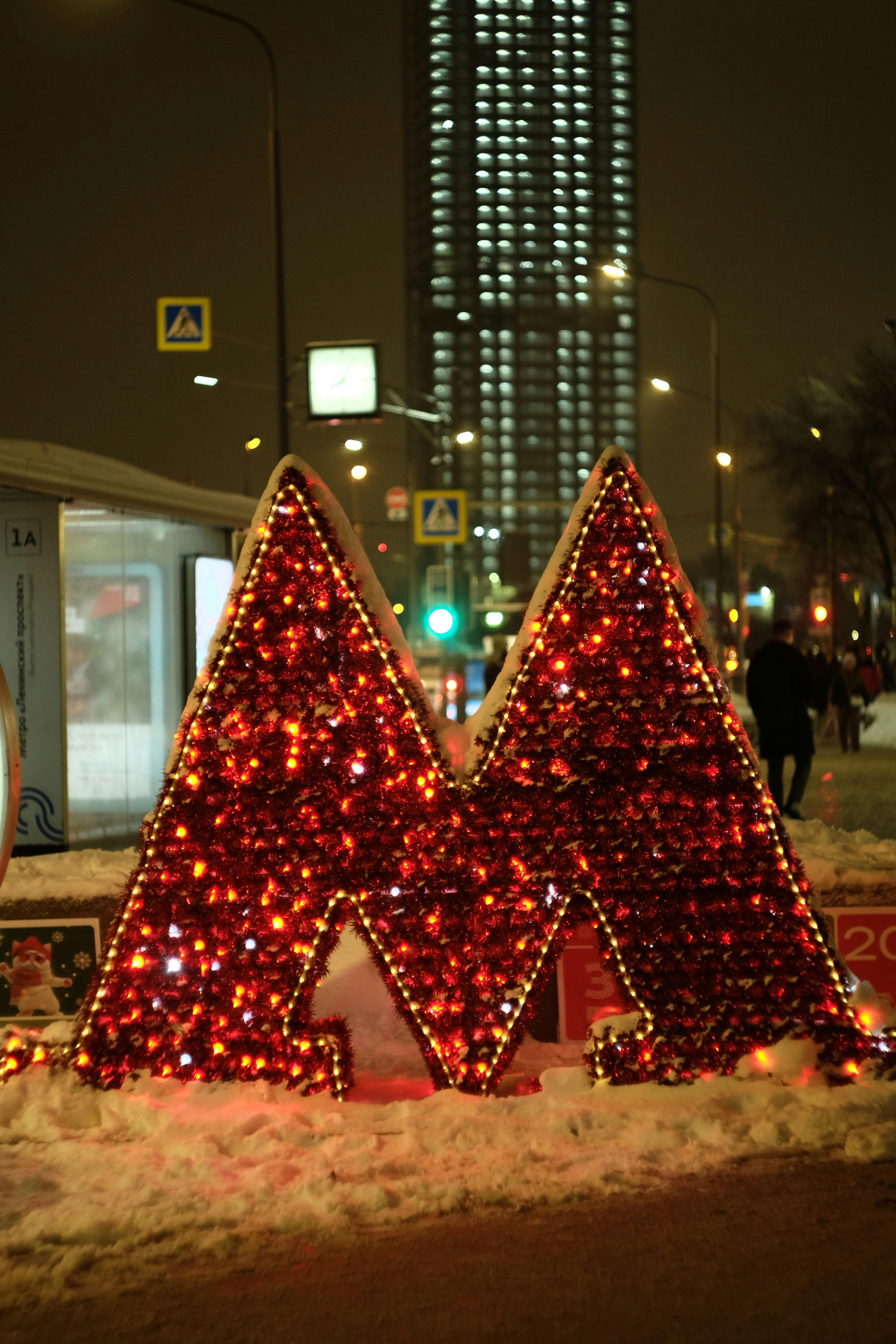 Neon-Outlined M-shaped Christmas sculpture glowing in the city night