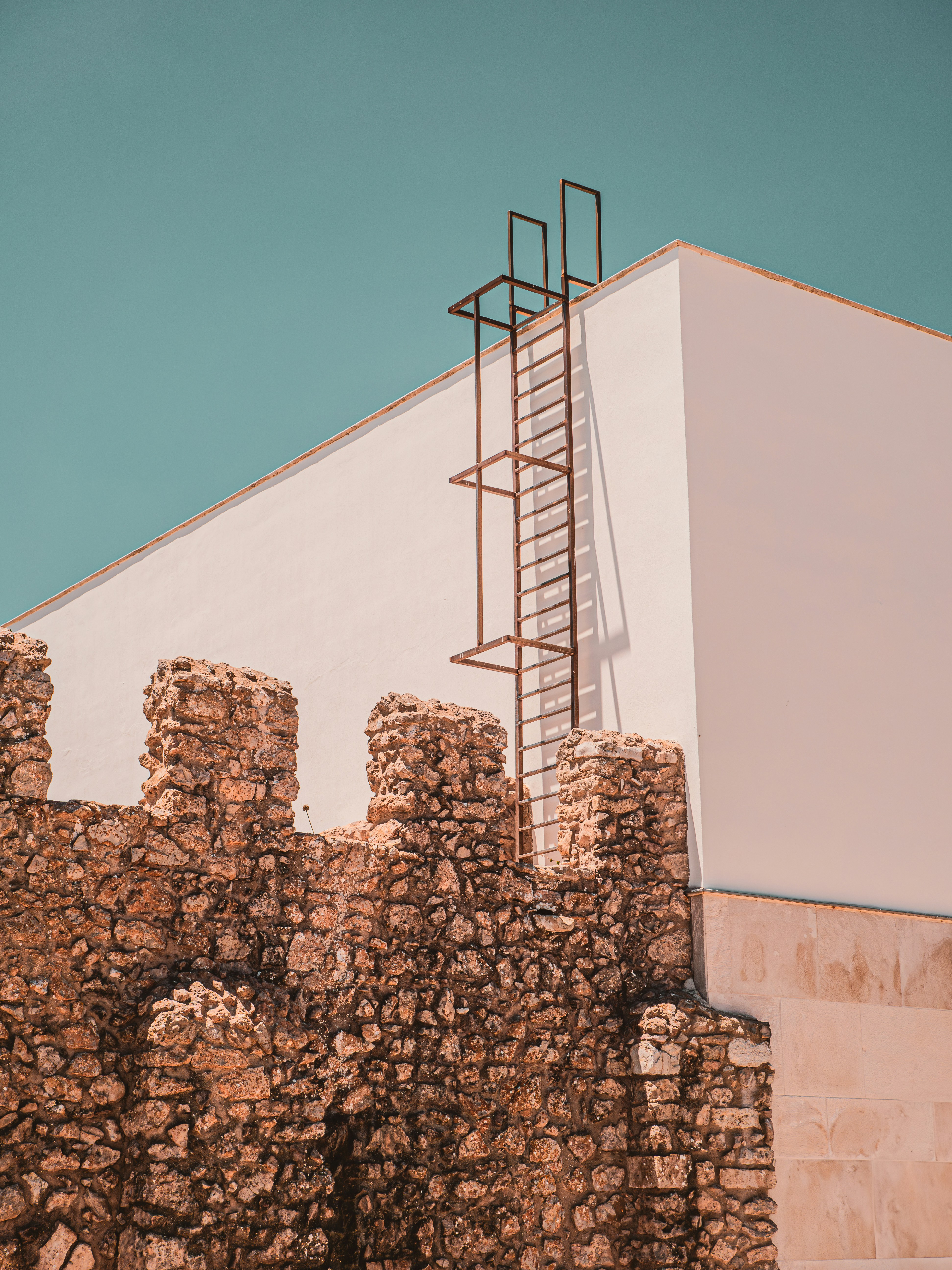 Rusted Ladder on a Modern Facade Rising Over Ancient Stones