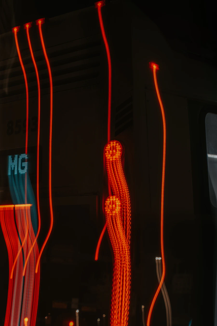 Long-exposure capture of neon light trails in an urban facade at night, creating abstract red streaks with subtle architectural hints in the background.