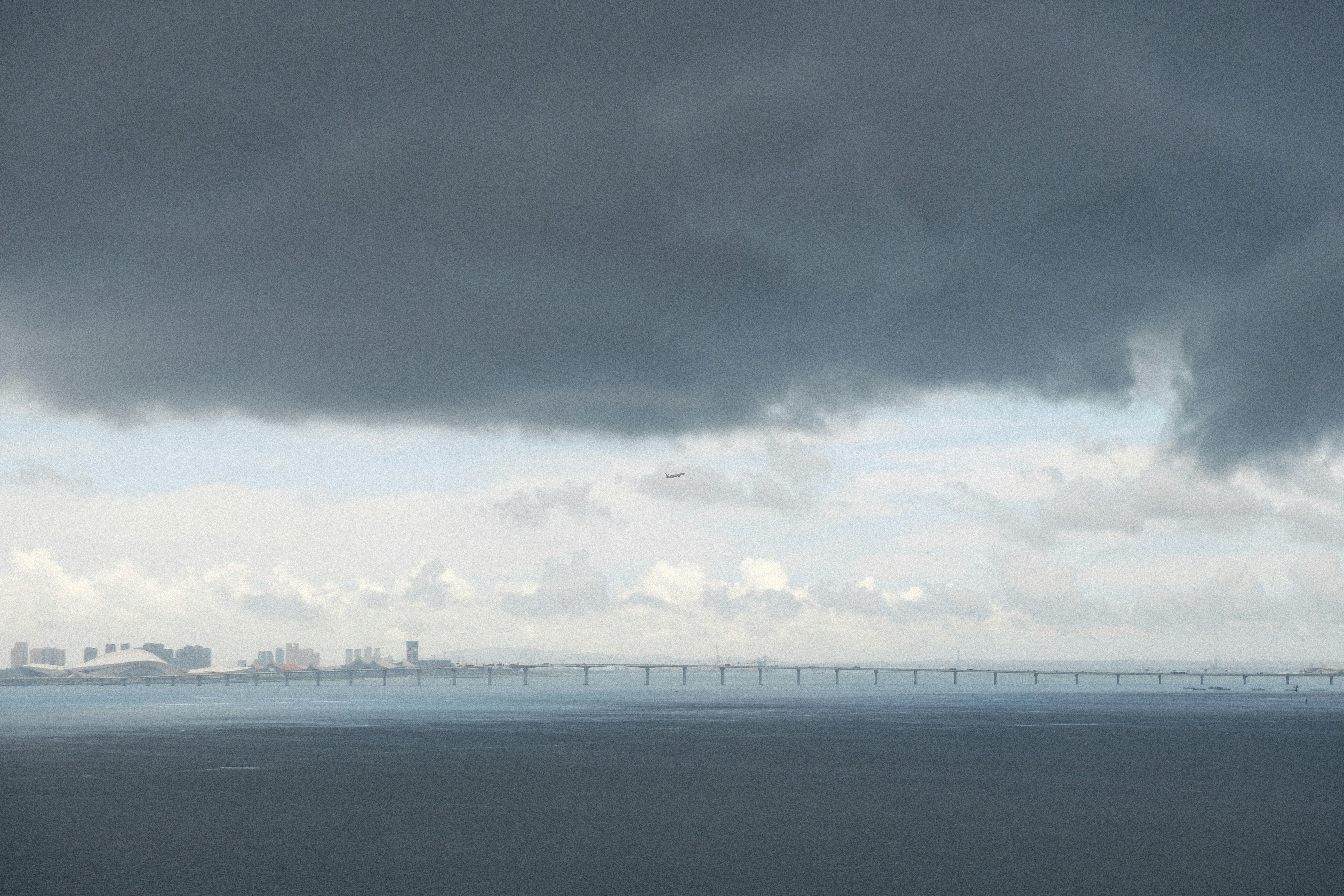 A long bridge stretches across the water under stormy skies. photo ...