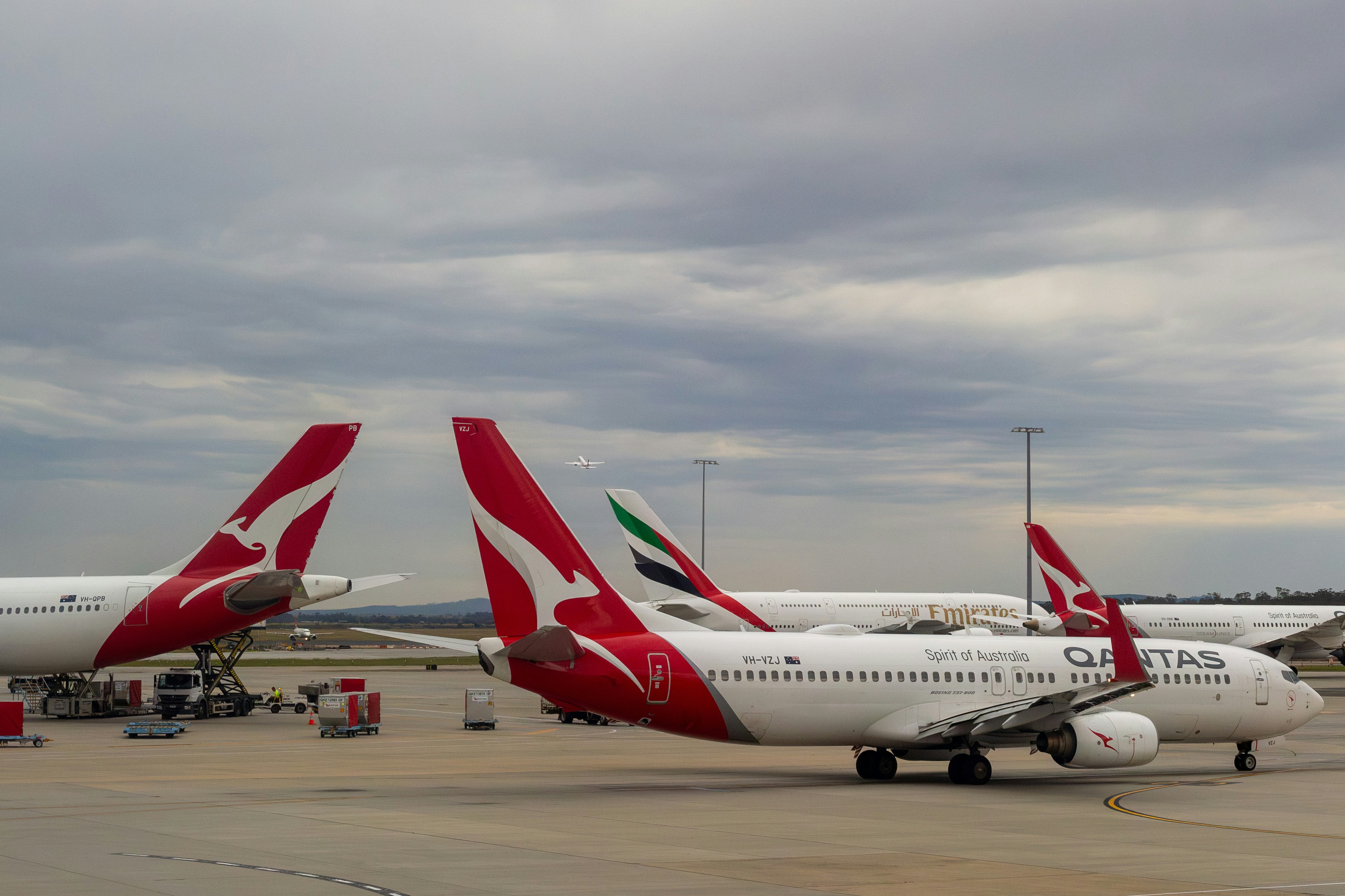 Red-tailed Qantas and Emirates shuttling at a sunlit tarmac