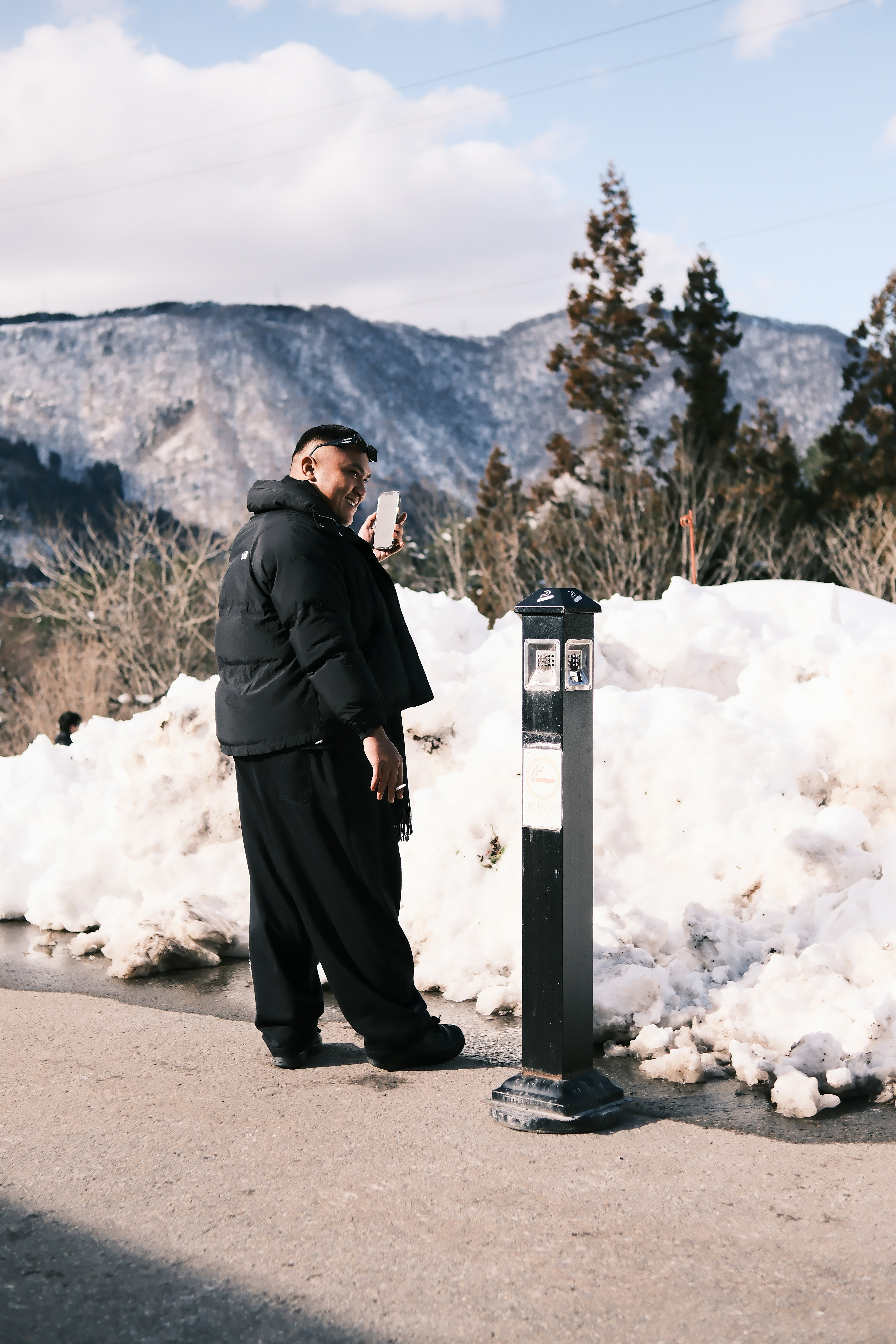 Snowy overlook selfie: a lone man in black coat engages his phone beside a height marker