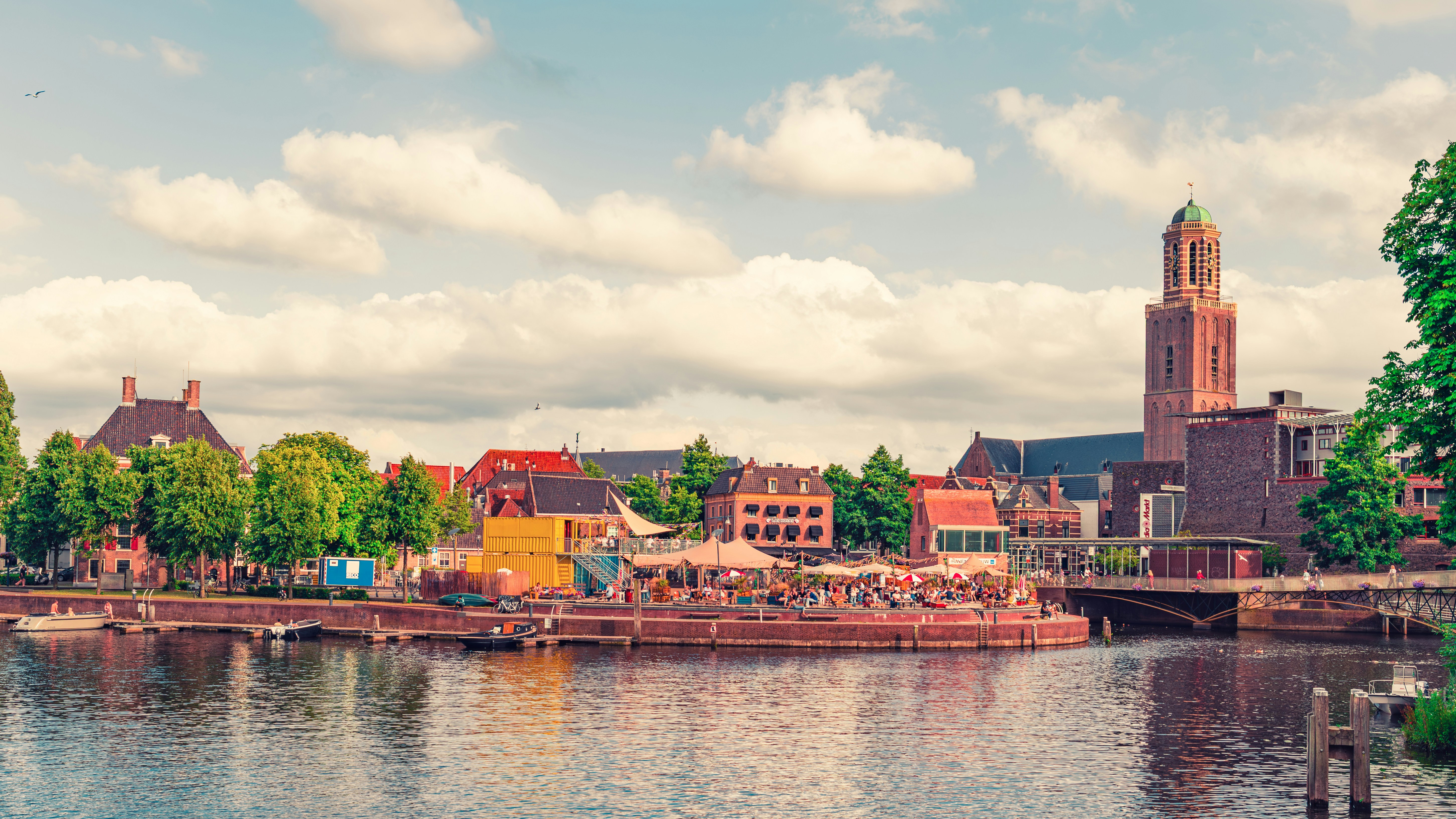 Series of photographs taken in Zwolle, Netherlands, depicting the city’s historic waterfront and lively urban atmosphere along the river and harbor area. The images feature the passenger ship Ooster Schelde moored along the quay, animated terraces and public gatherings by the water, and the distinctive skyline marked by the Peperbus tower of the Basilica of Our Lady of the Assumption. Reflections on the calm water, brick architecture, and evening light highlight Zwolle’s identity as a historic Hanseatic city where heritage, leisure, and contemporary urban life coexist.