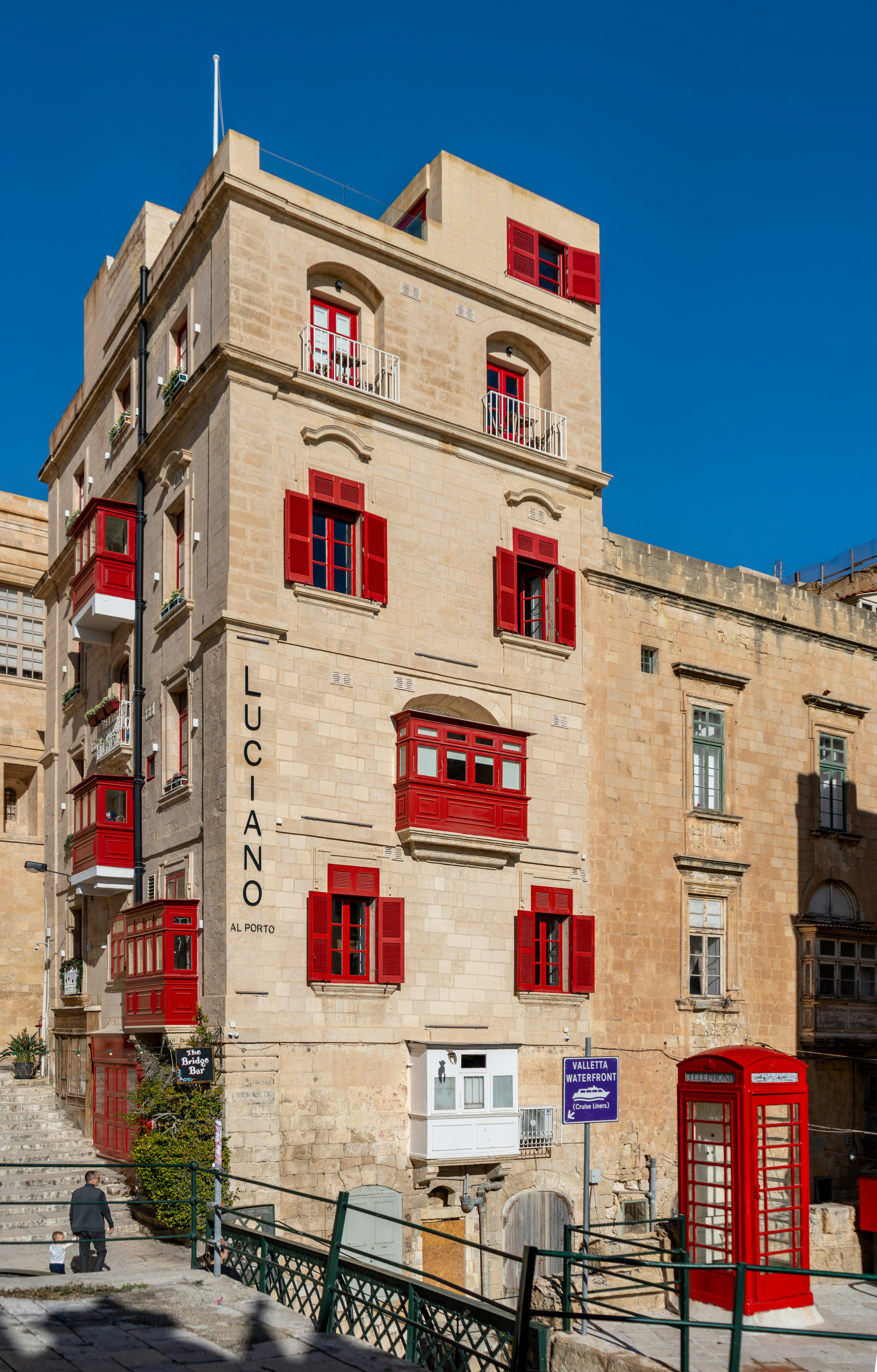 Sunlit limestone façade with red shutters and a classic red telephone booth