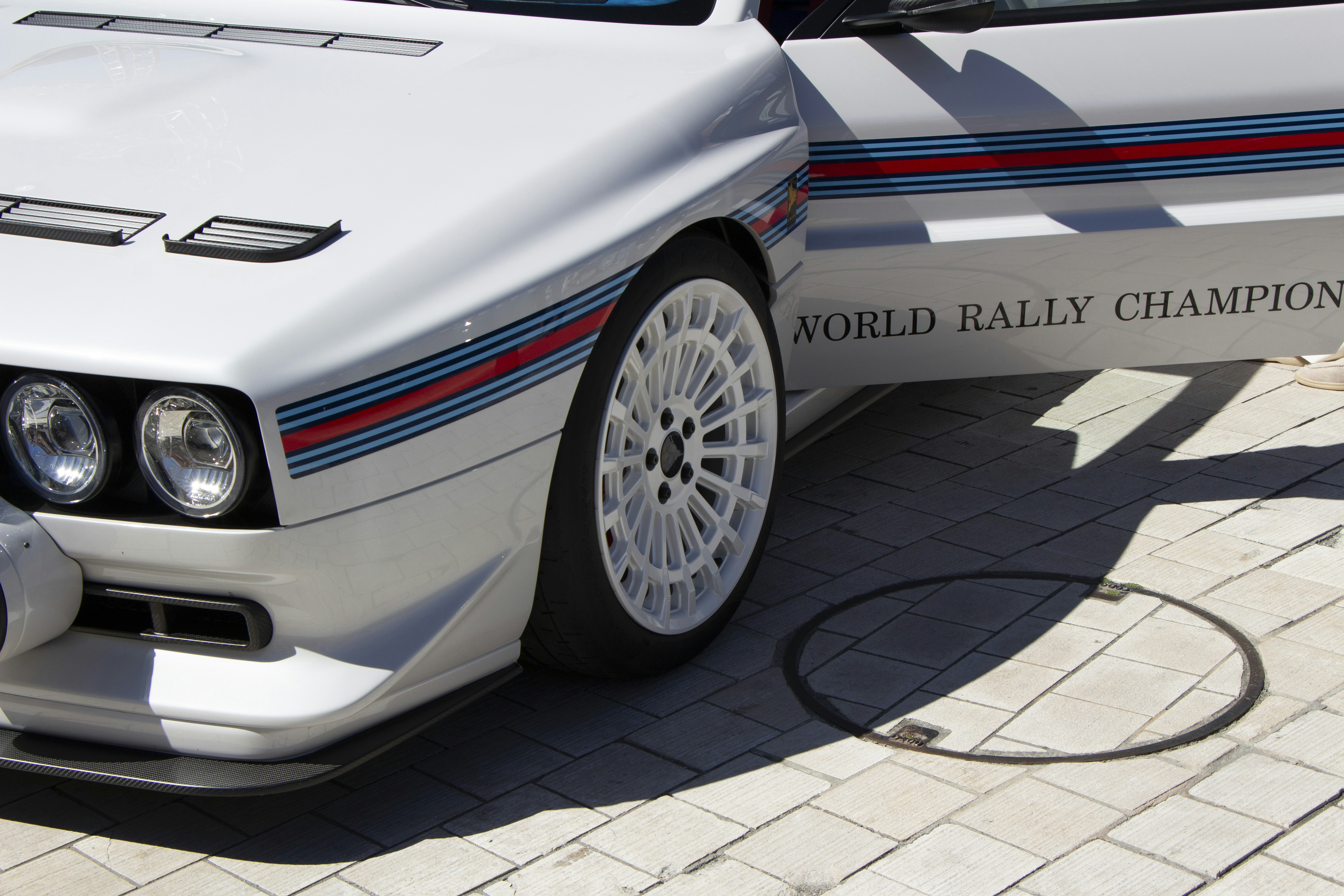 White rally car with blue-red striping and engraved 'World Rally Champions' on tiled pavement