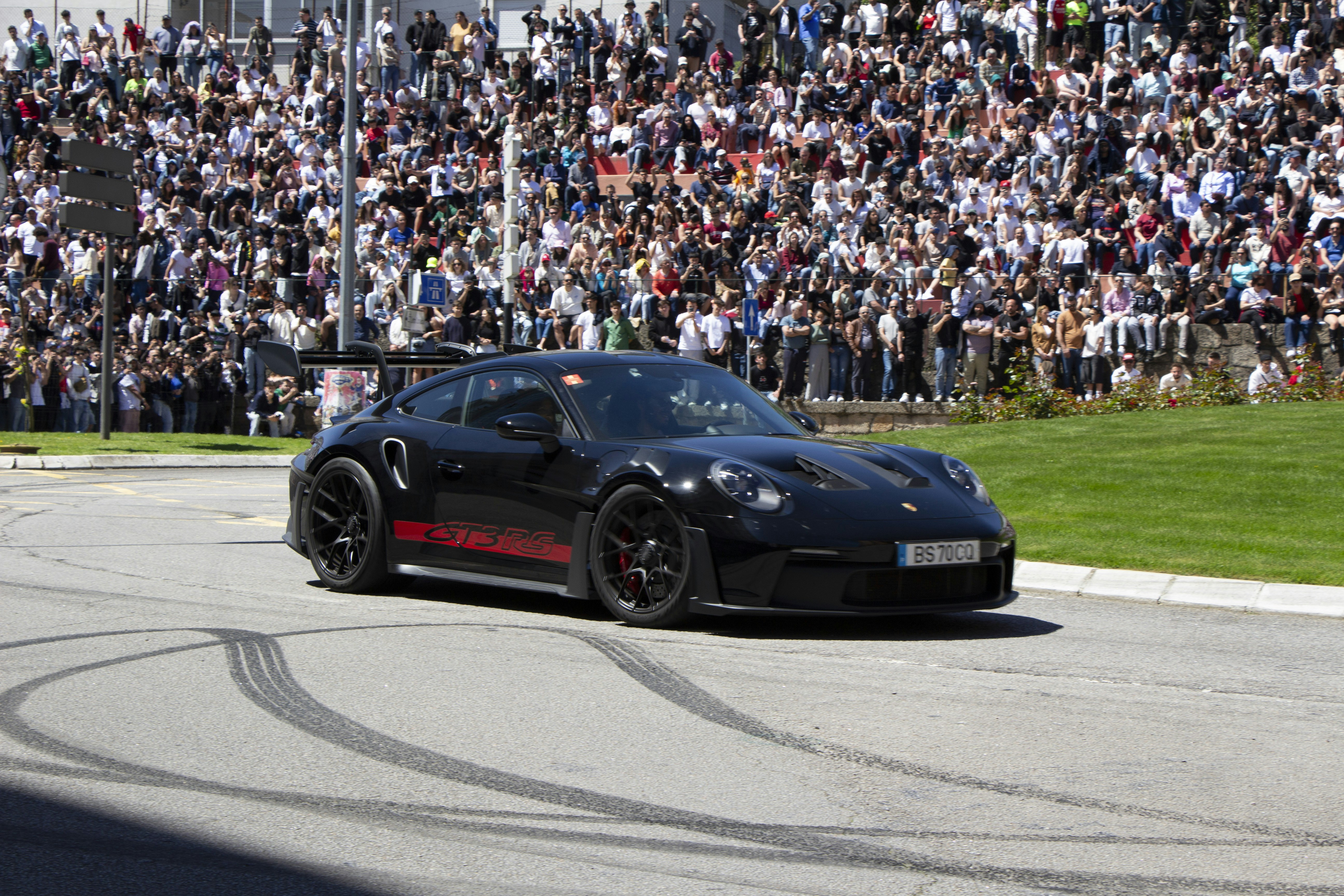 Black Porsche Surges Past a Roaring Crowd at a Street Parade
