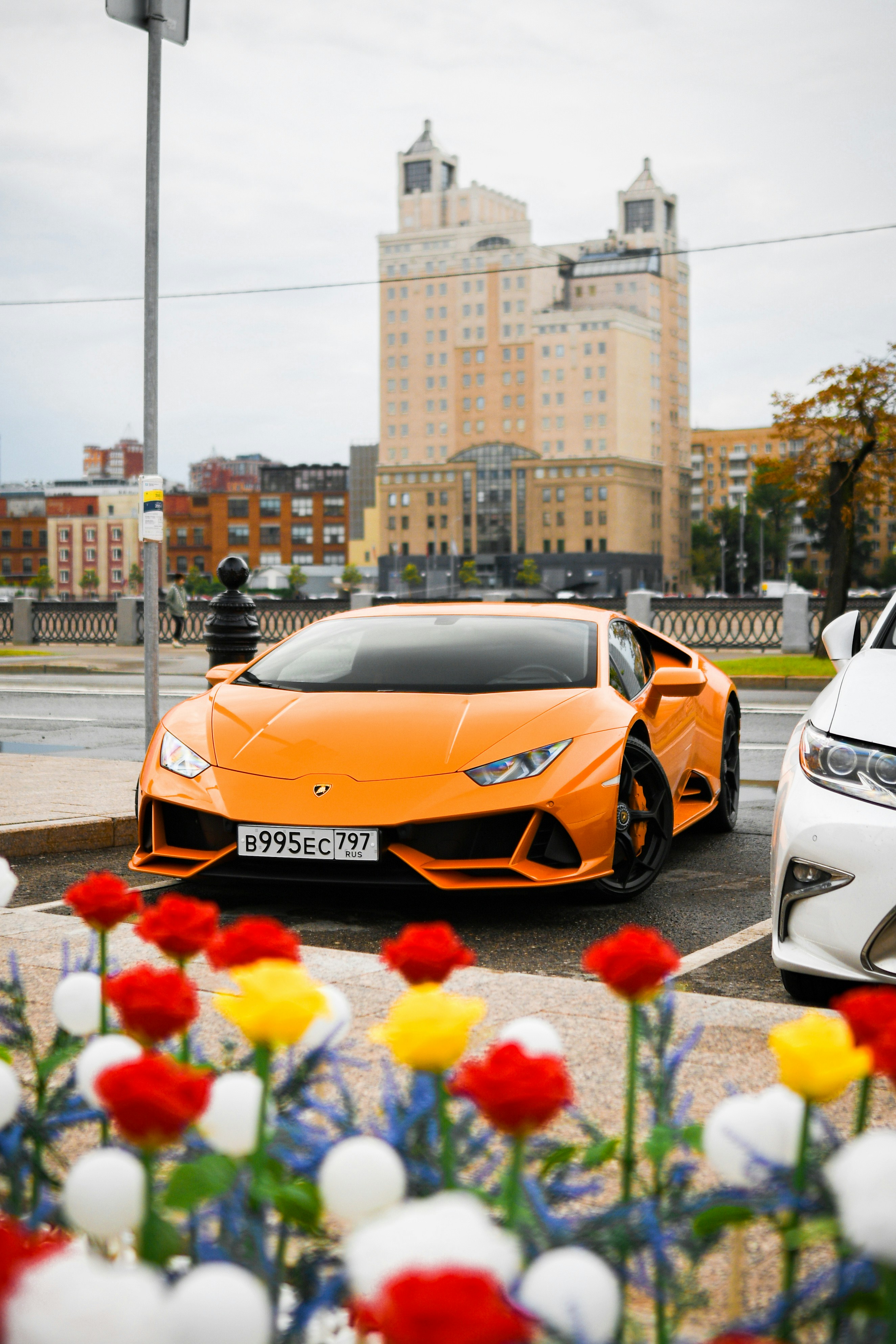 Orange Lamborghini in urban harborfront with colorful foreground blooms