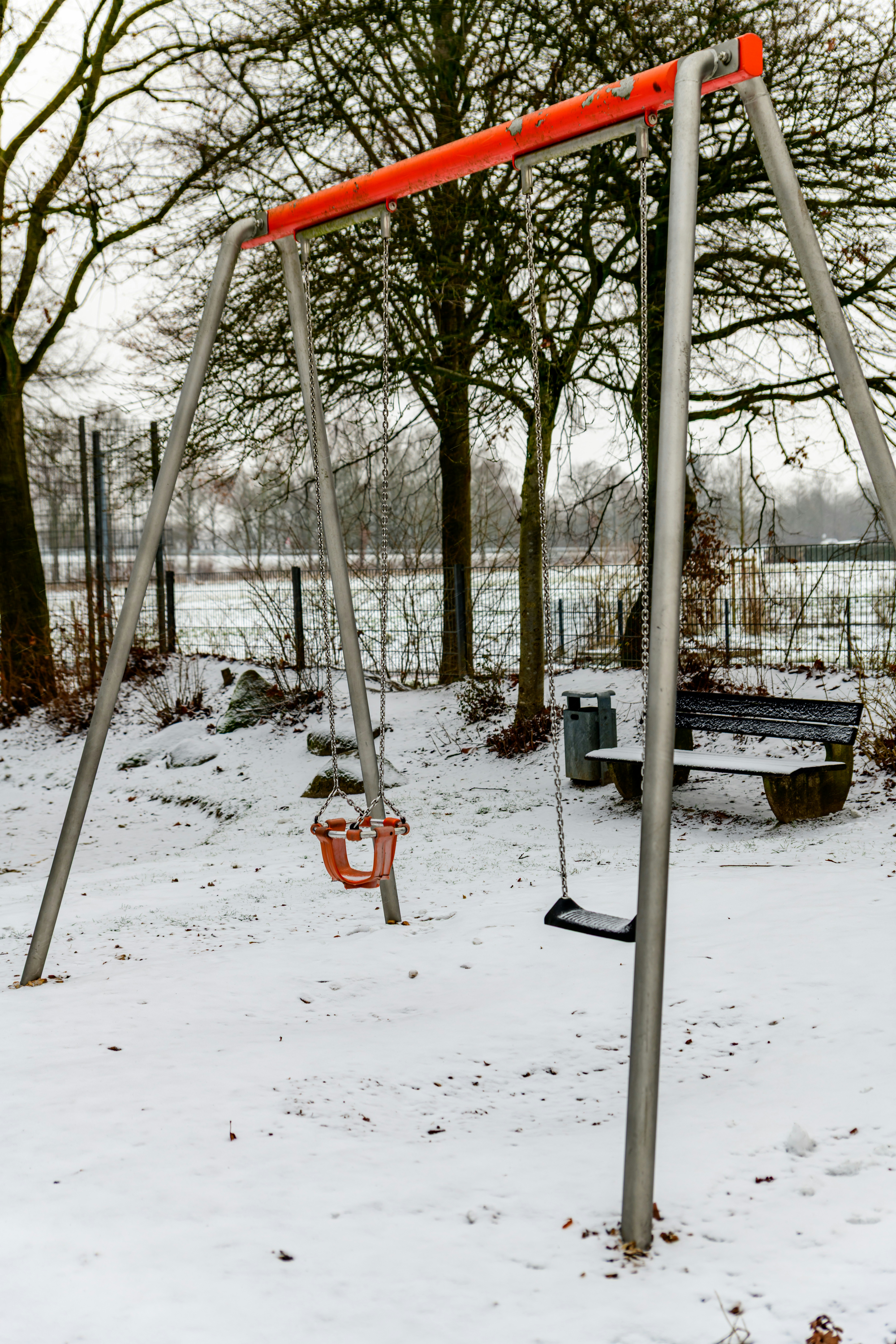 Snow-Quiet playground: orange swing set beneath a winter hush
