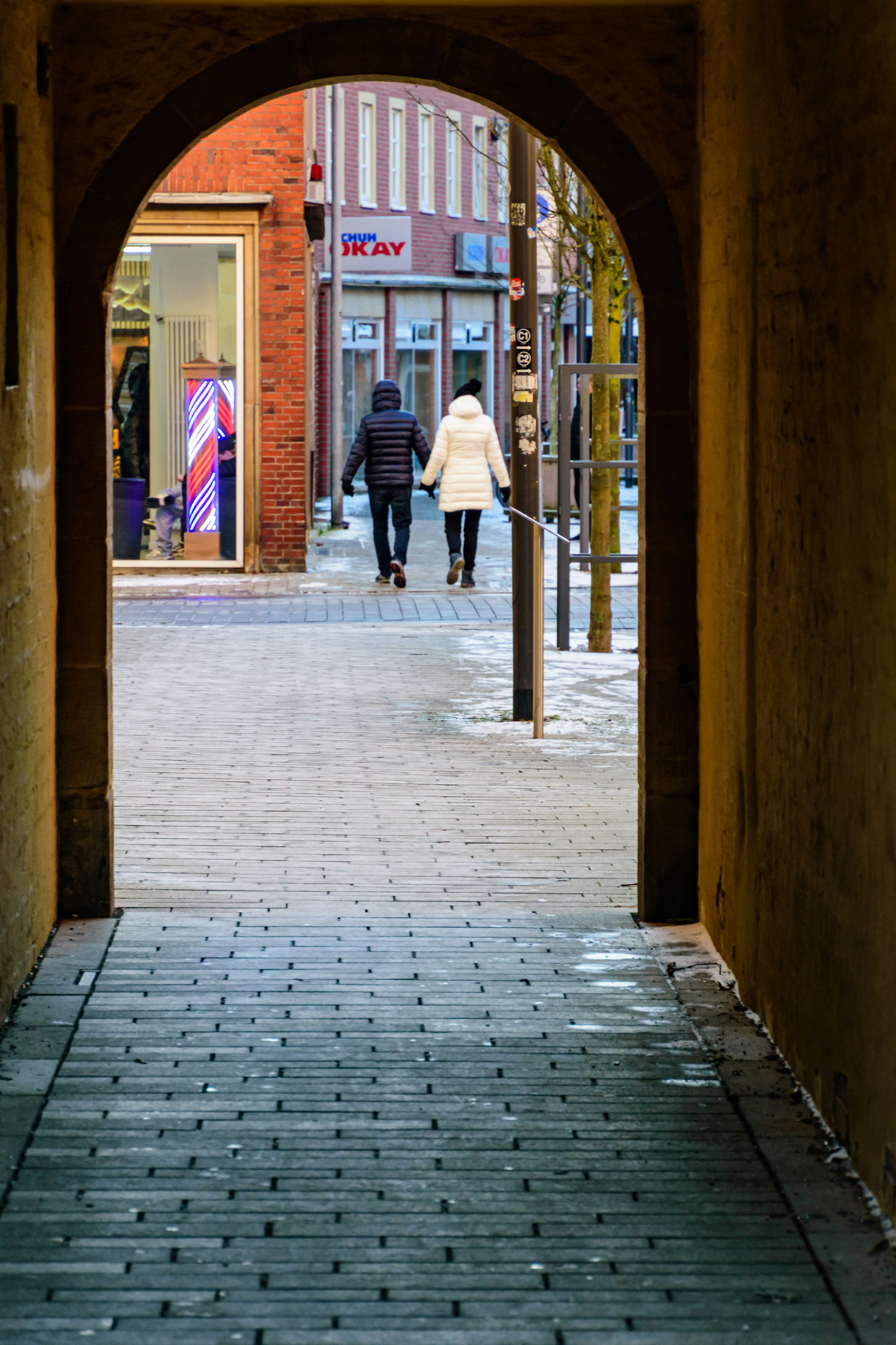 Through the Archway: Two Seemingly Ordinary Walkers Framing a City Corridor