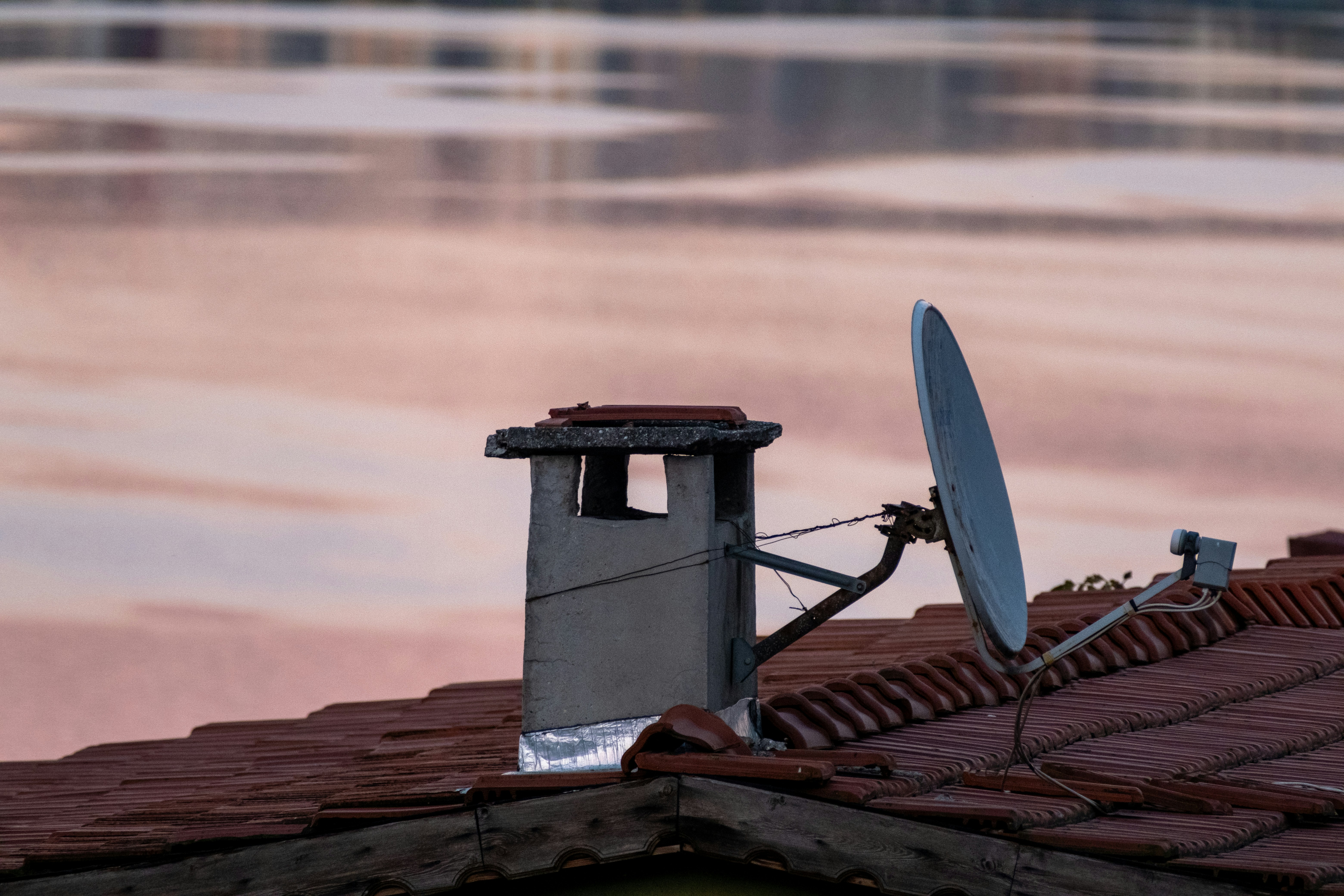 Satellite on a Shingled Rooftop under a Soft Sunset