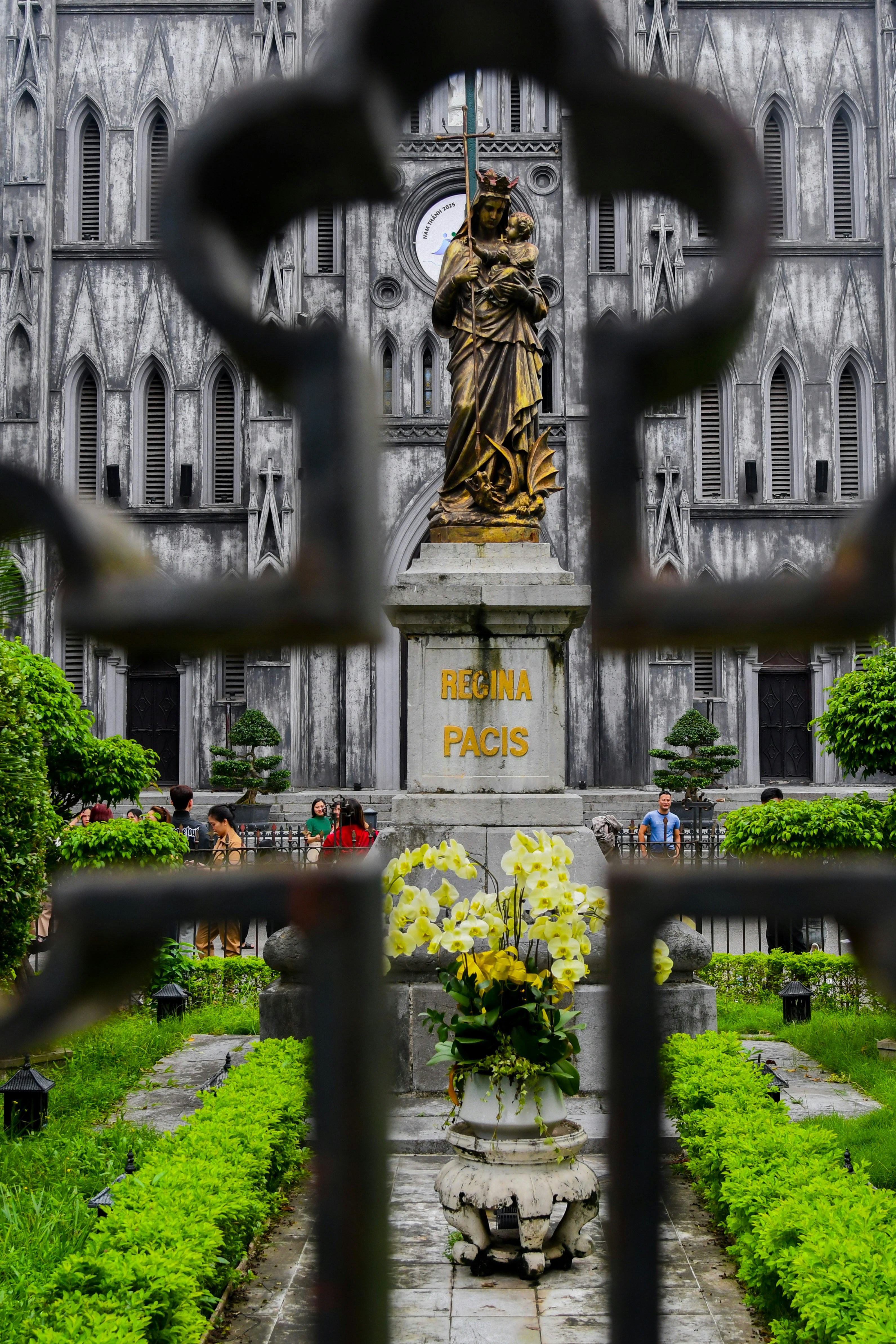 Statue of Regina Pacis framed by a historic façade, through wrought-iron lattice