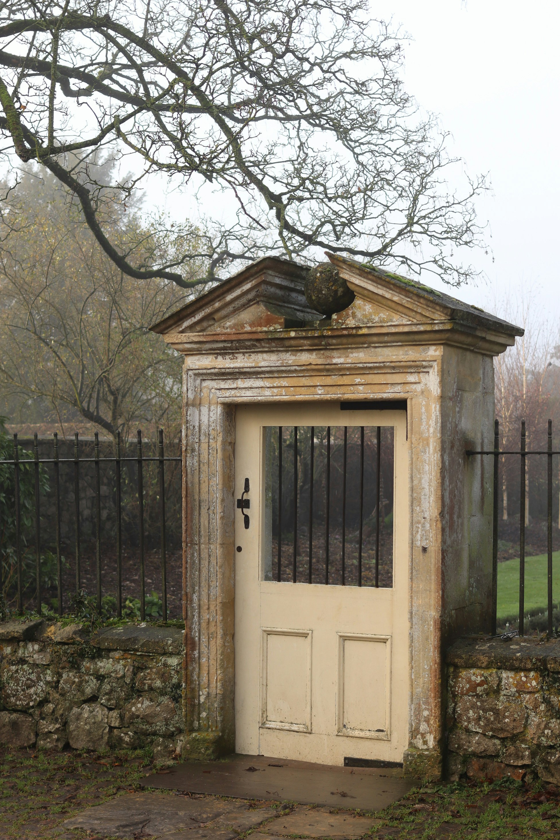 A Gatekeeper in Weathered Stone: The Small Door Standing Between Gardens and Time
