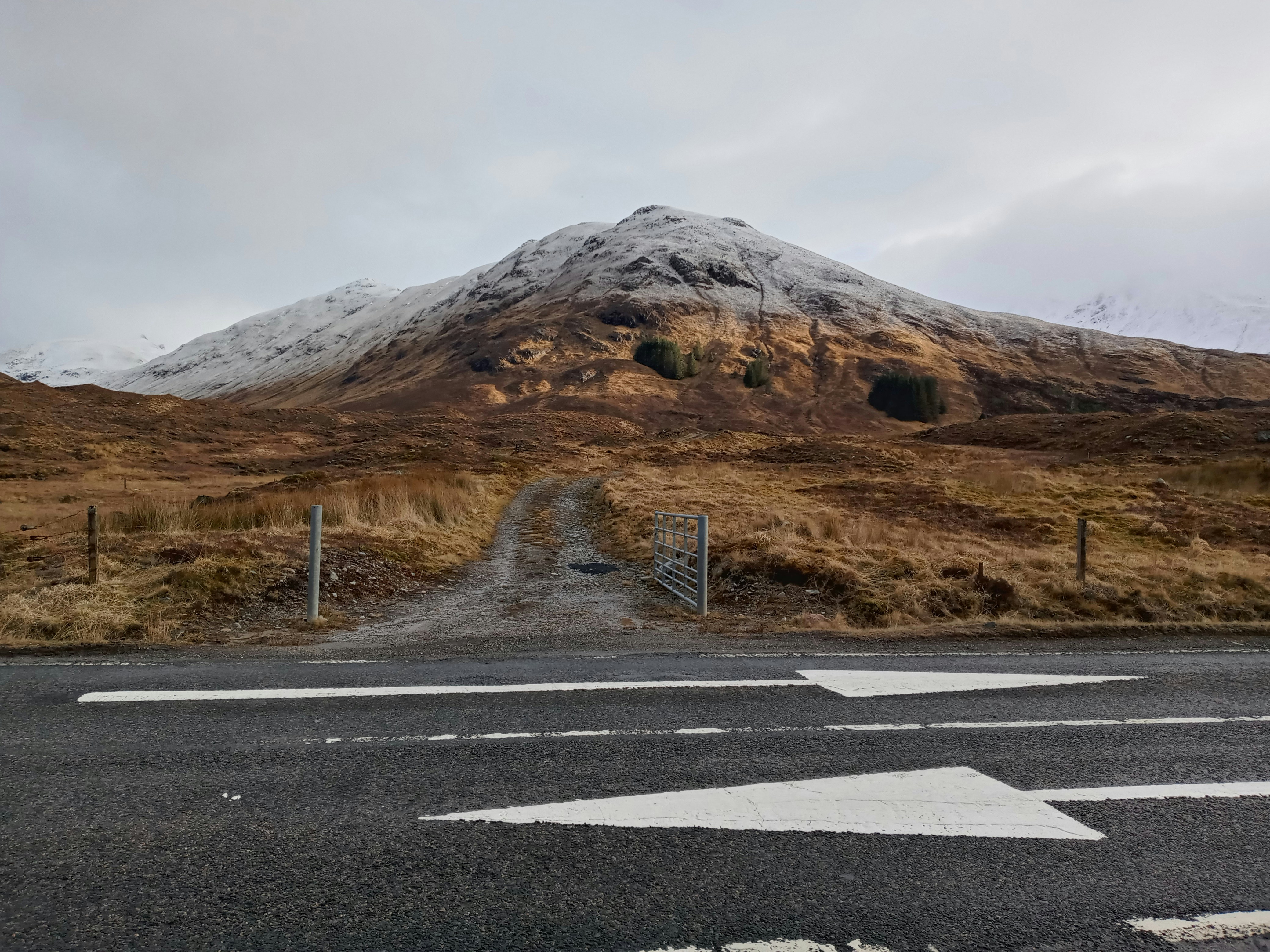 Snow-dusted mountain overlooks a grassy path and rocky landscape.