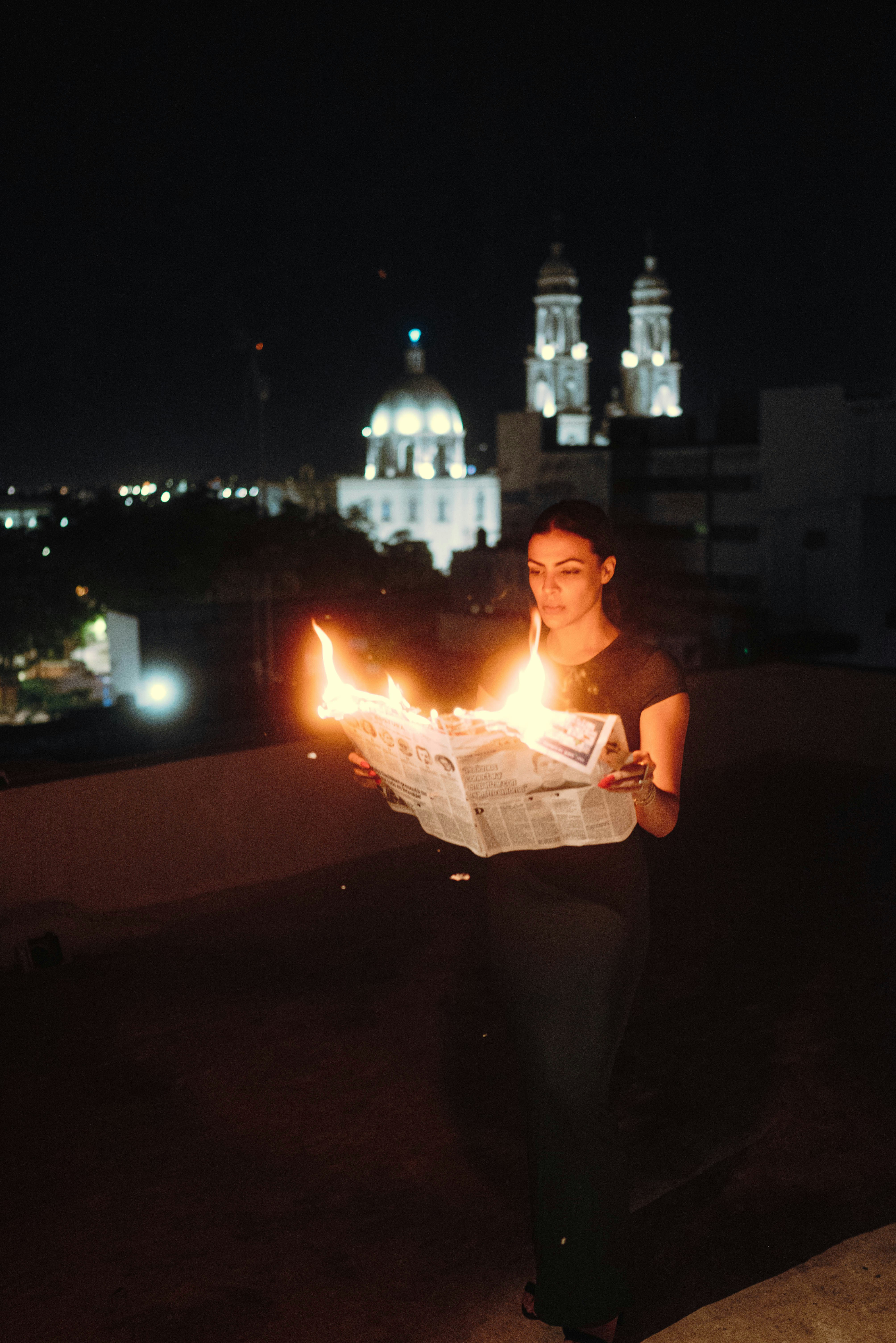 Night News: Flame-lit Newspaper Readings on a Rooftop