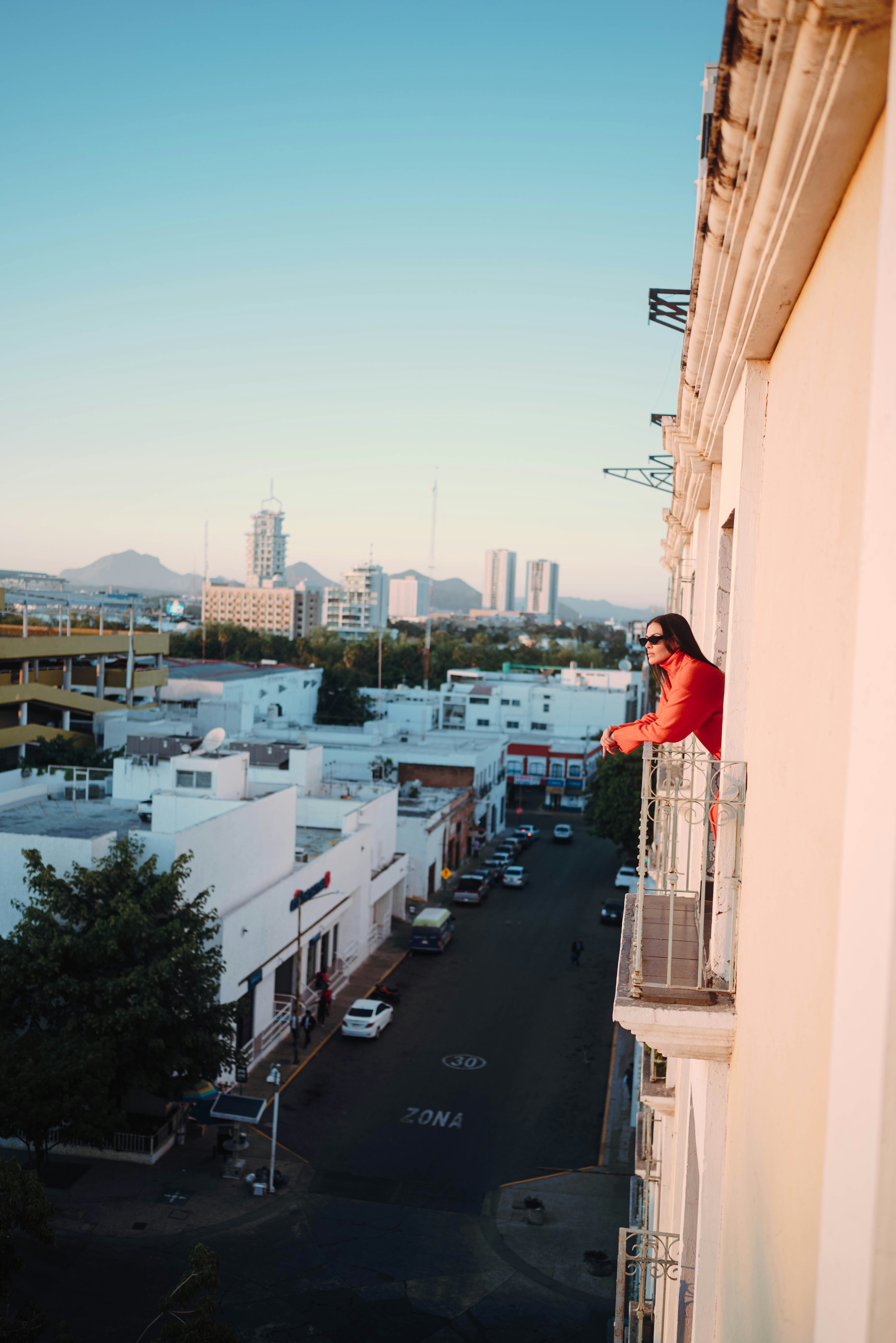Red-clad observer on a sunlit balcony over a sunlit street