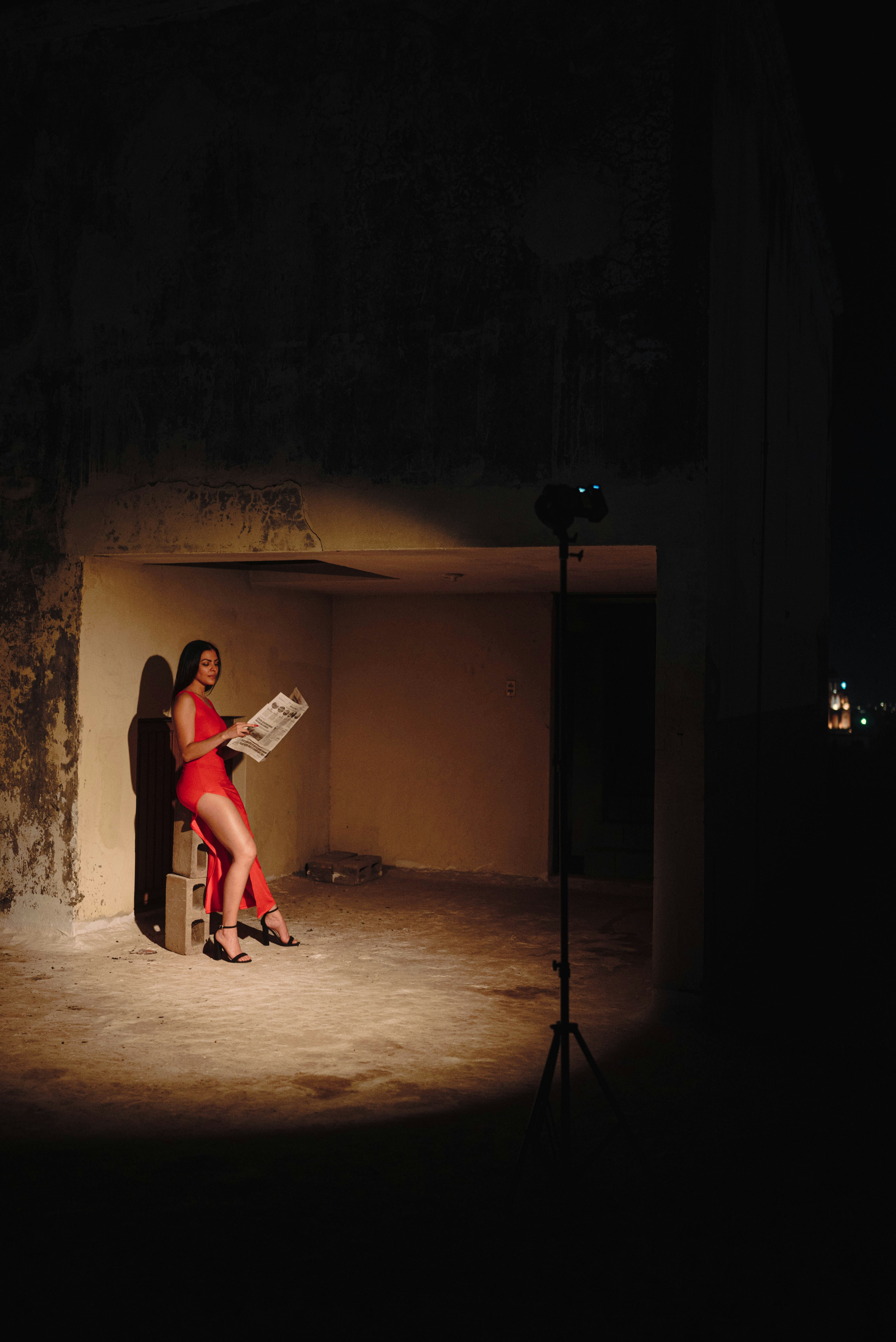 Woman in red dress reading newspaper in dimly lit room