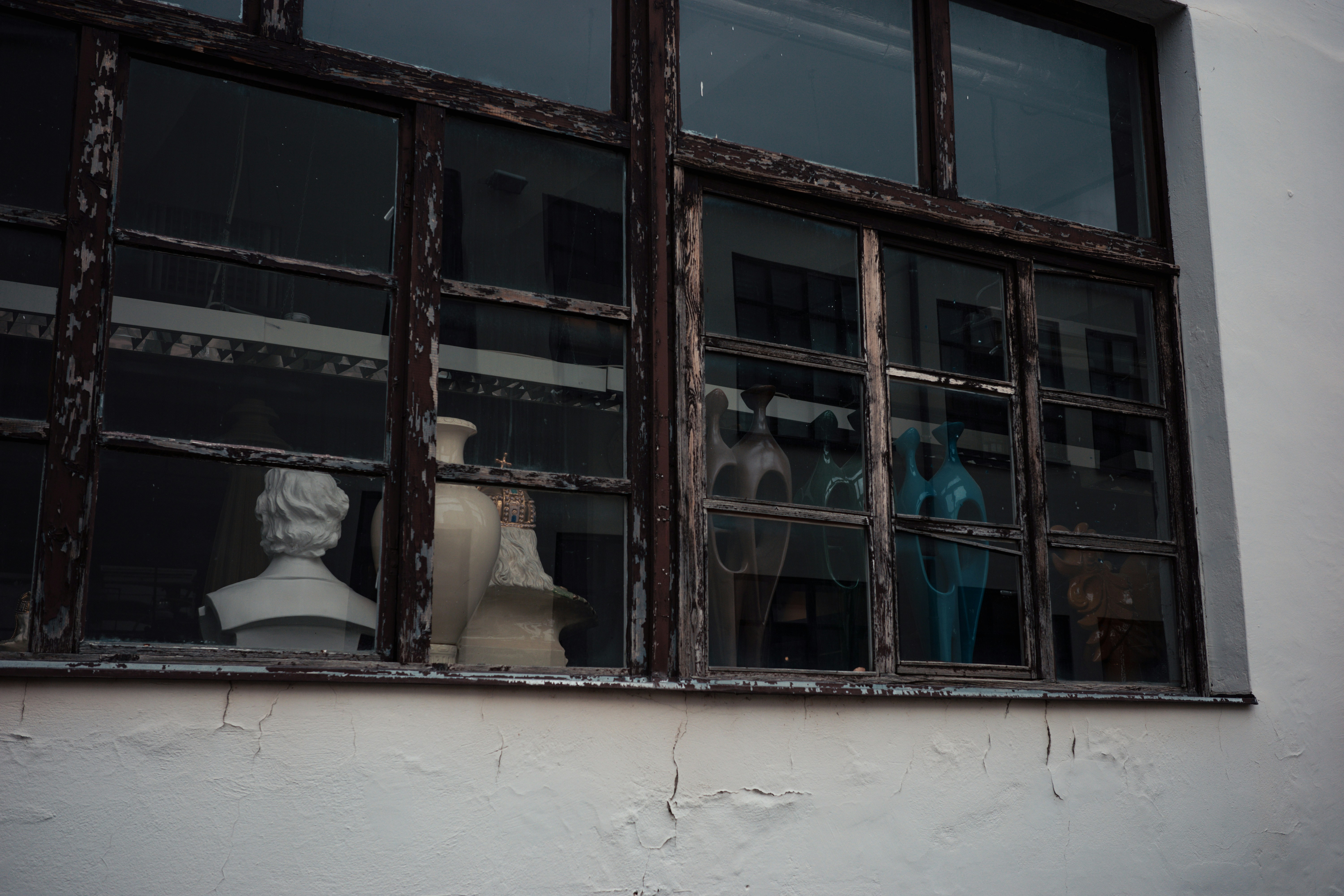 Aged storefront window with mannequin silhouettes under muted light