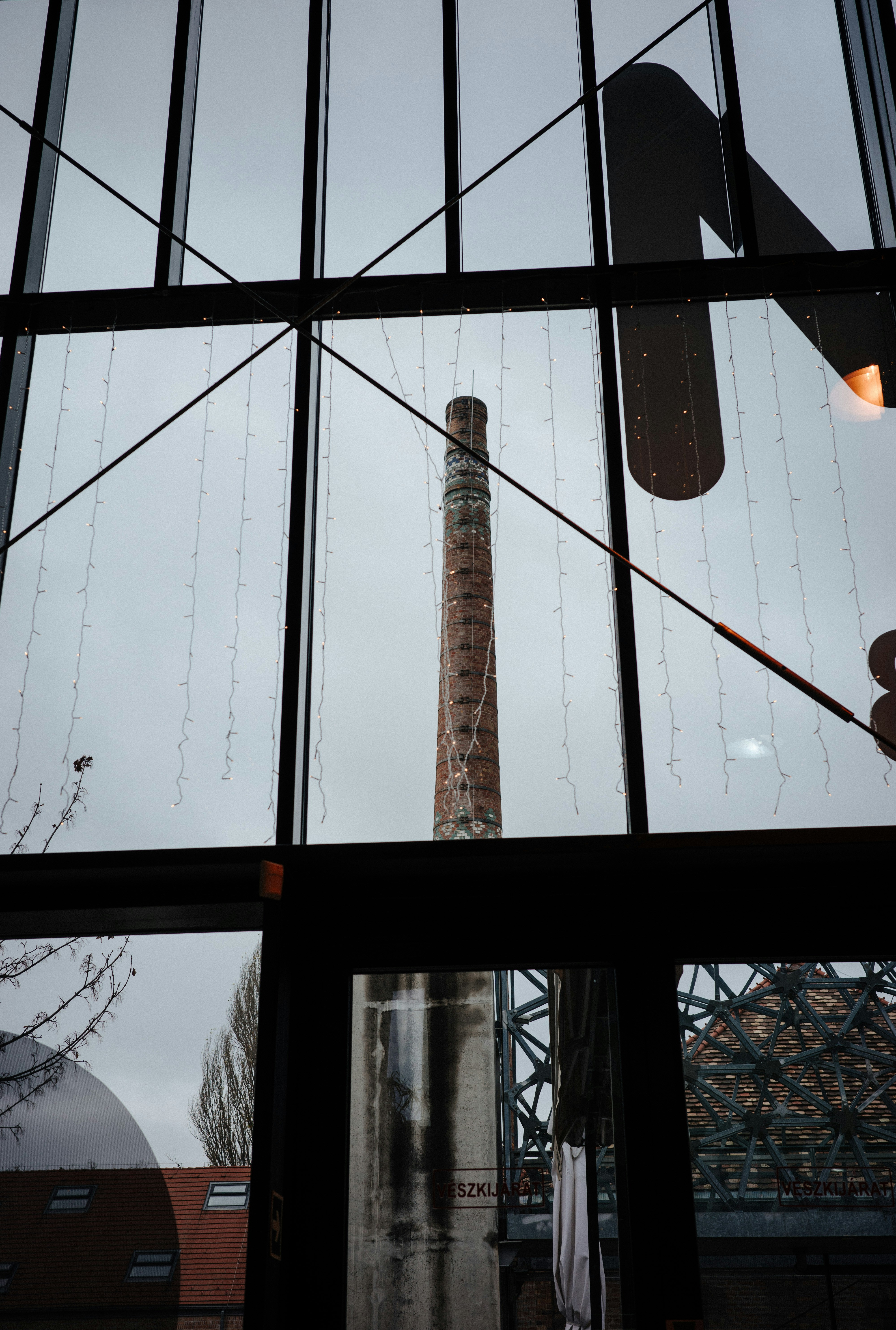 Industrial silhouette through glass: a city chimney framed by decorative lights
