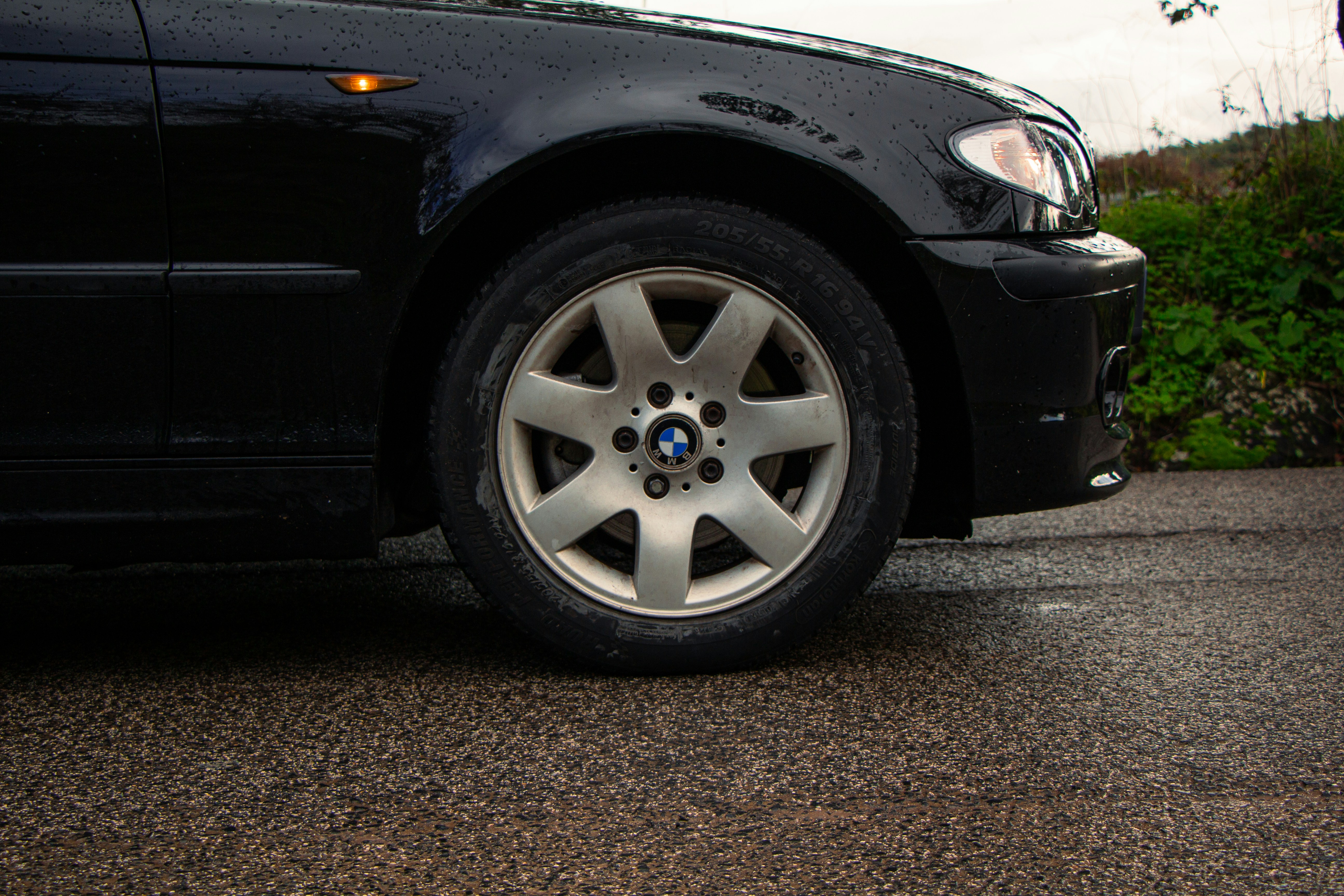 Dark sedan’s front wheel anchors a rain-kissed road
