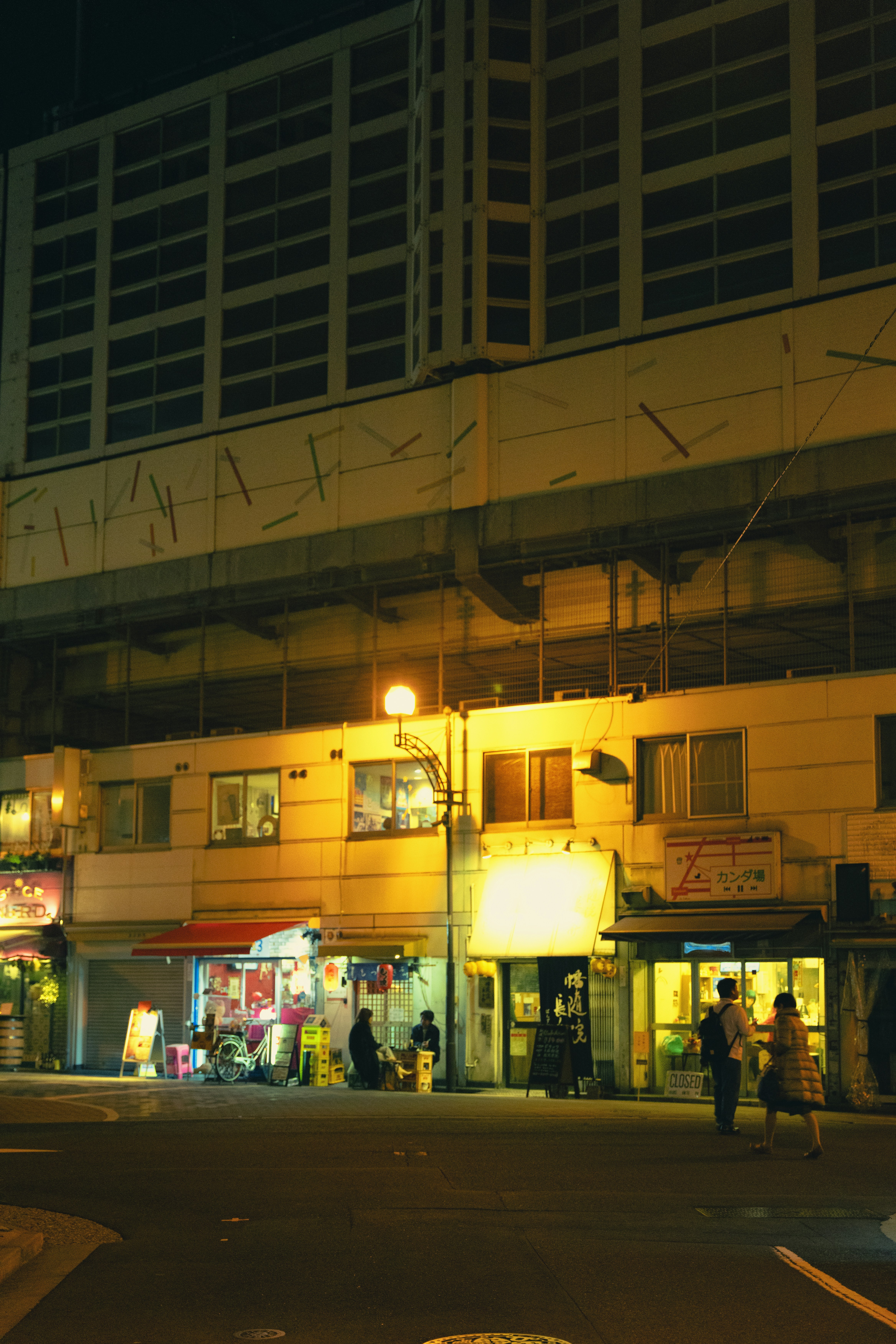Nightlife Below Neon Facade: Quiet Figures by the Street