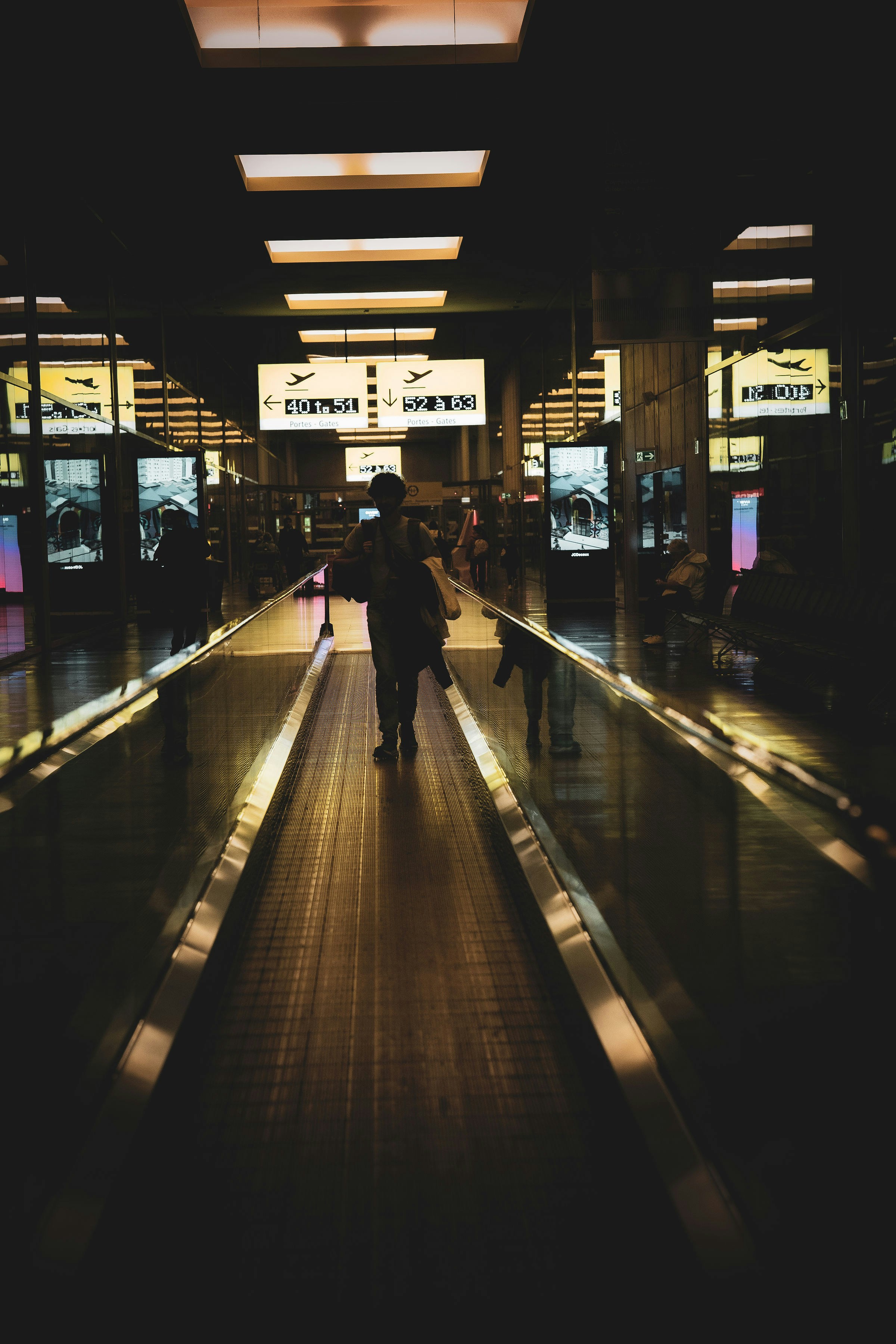 Midway on the Moving Walk: A Lone Figure in Neon Reflections