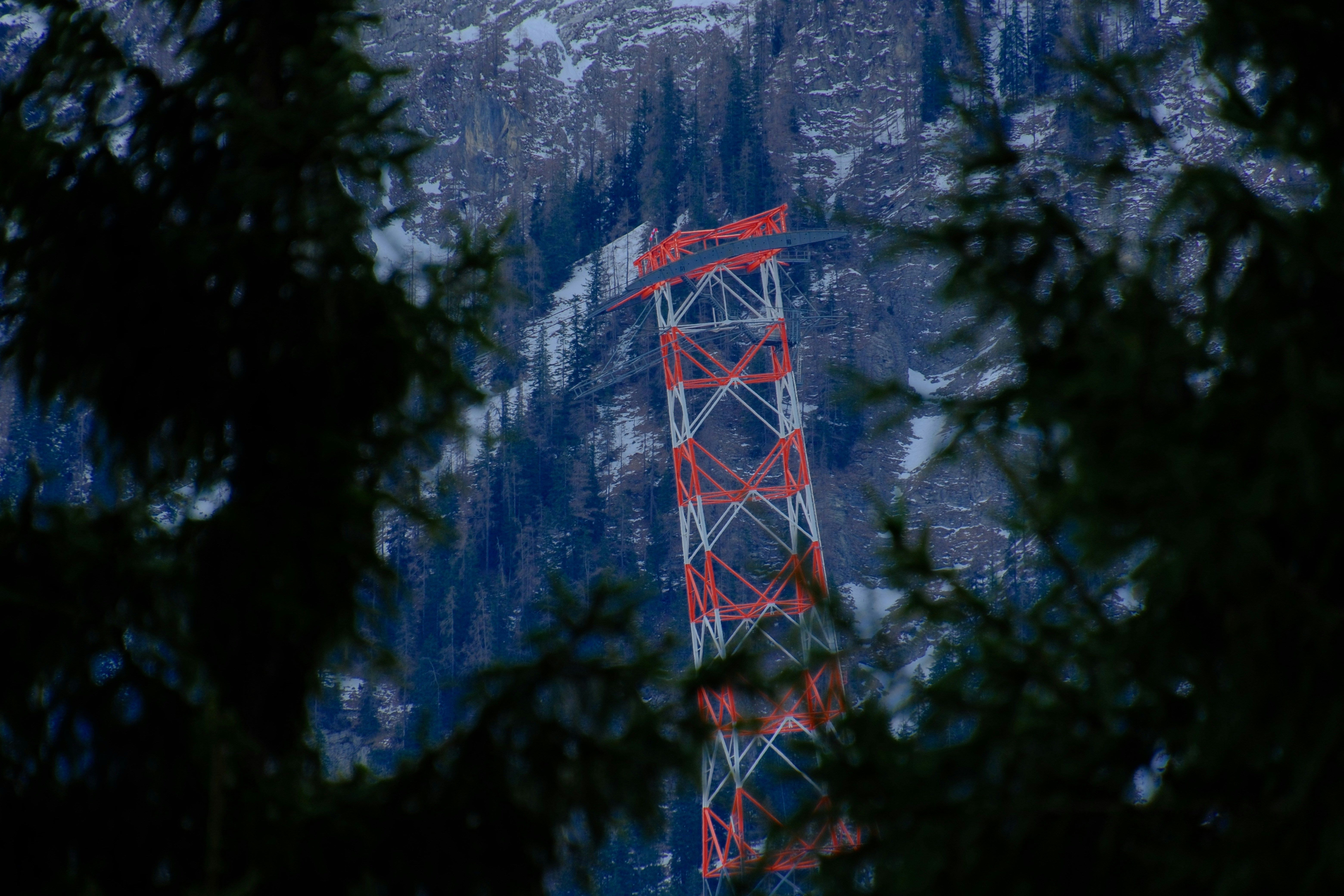 Red lattice tower peering through dark pines in a wintry valley