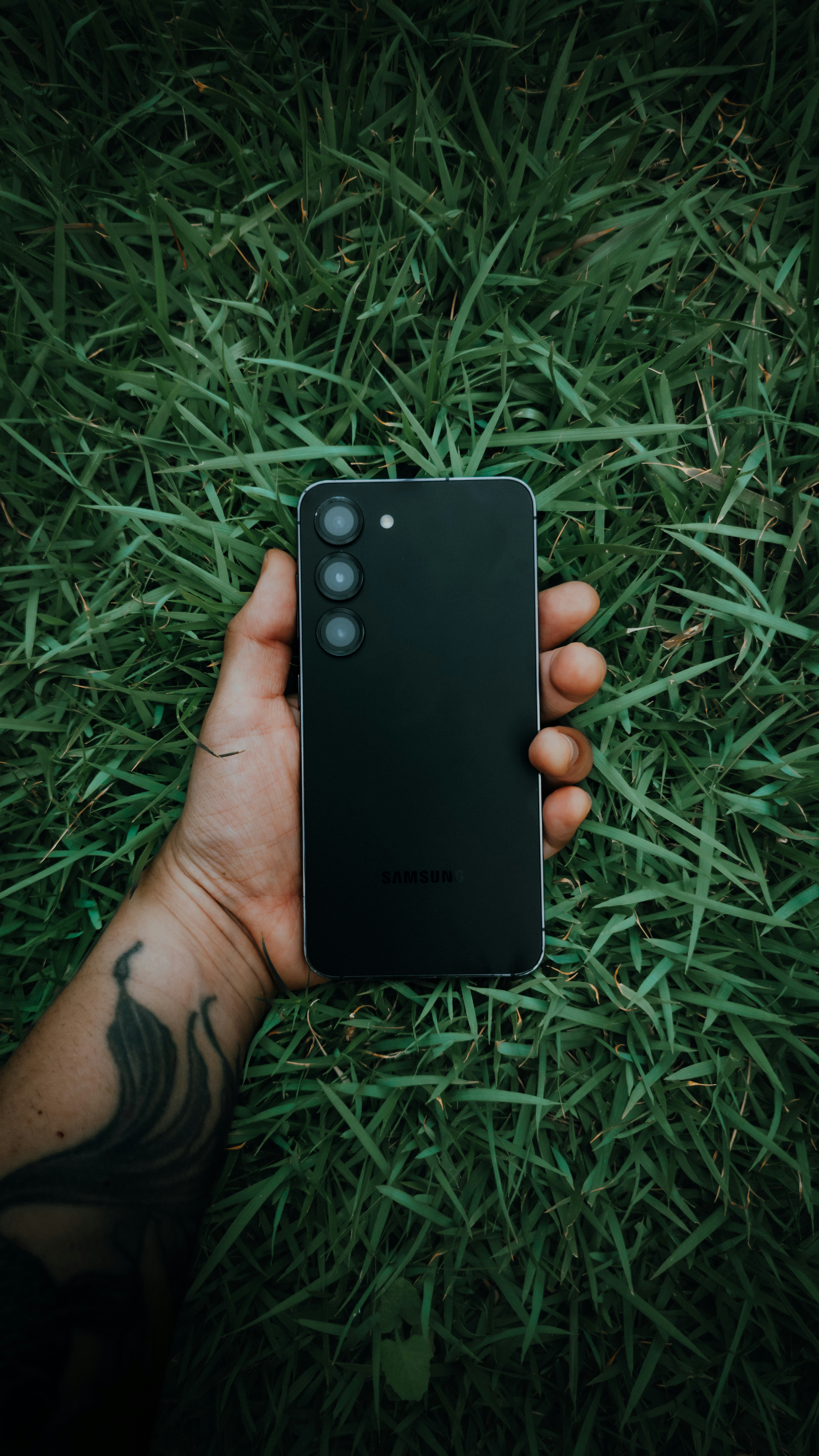 Hand holding a black smartphone over green grass.