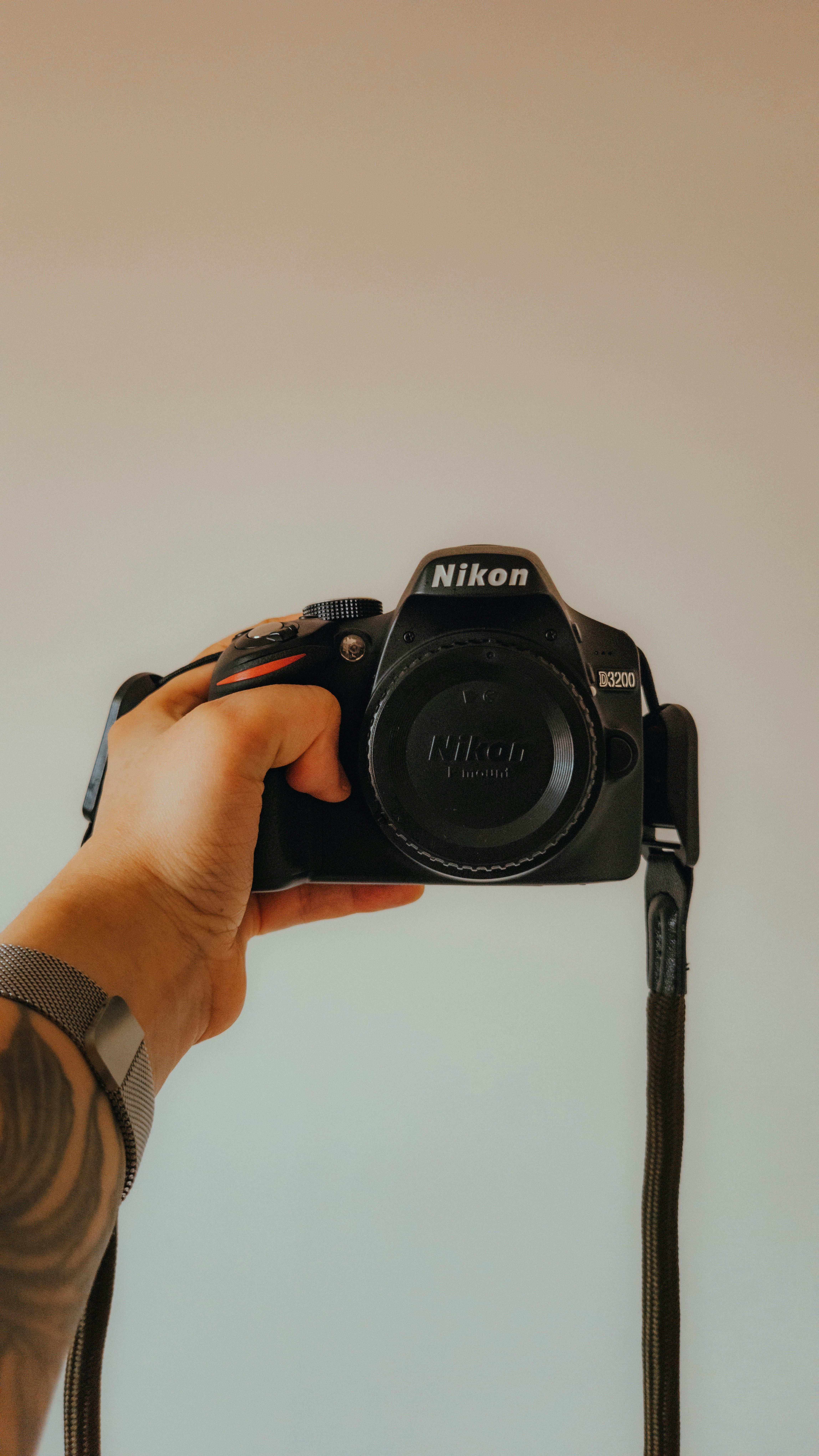 Hand holding a black nikon camera with strap