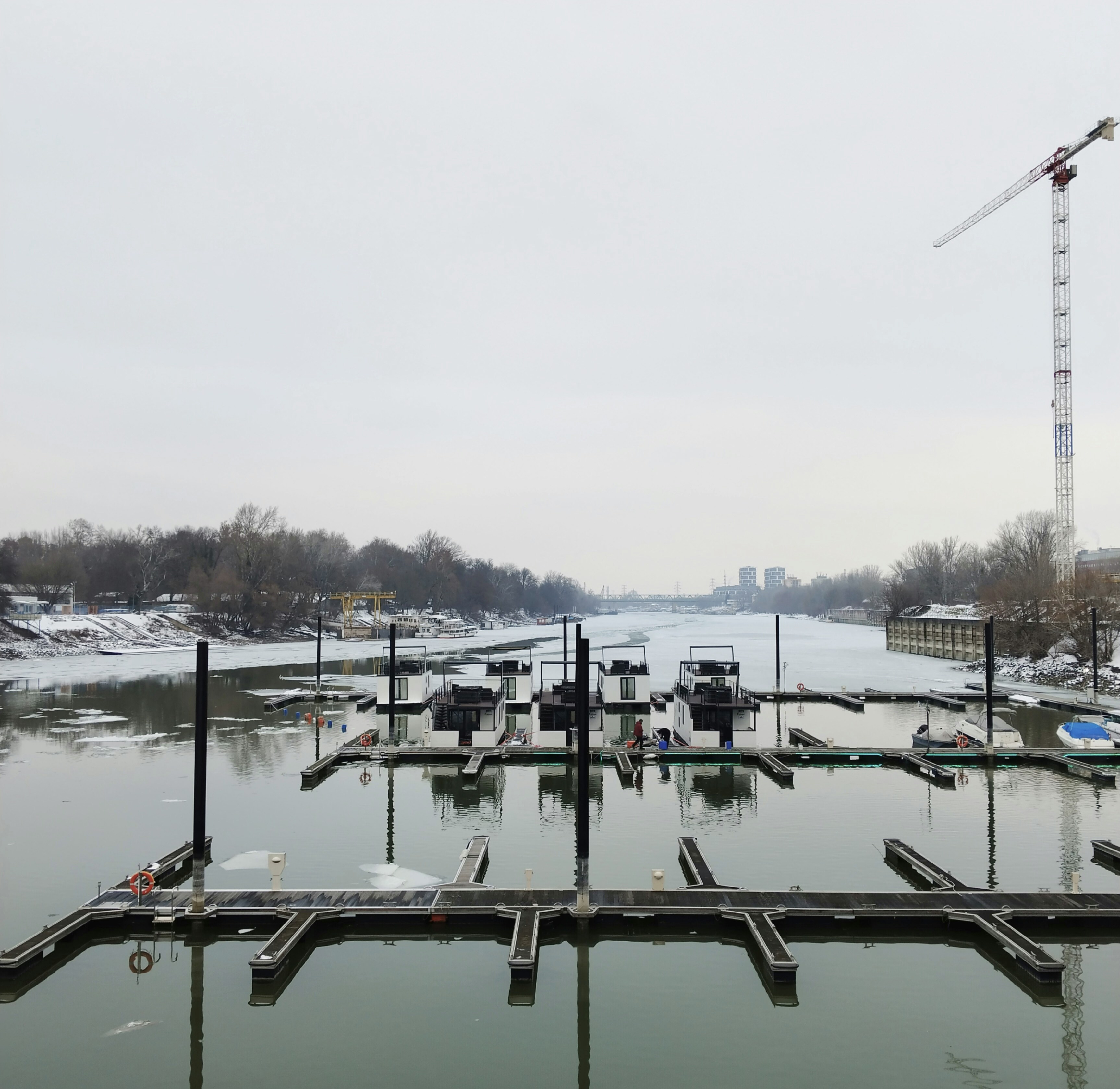 Boats docked in a frozen marina with a crane.