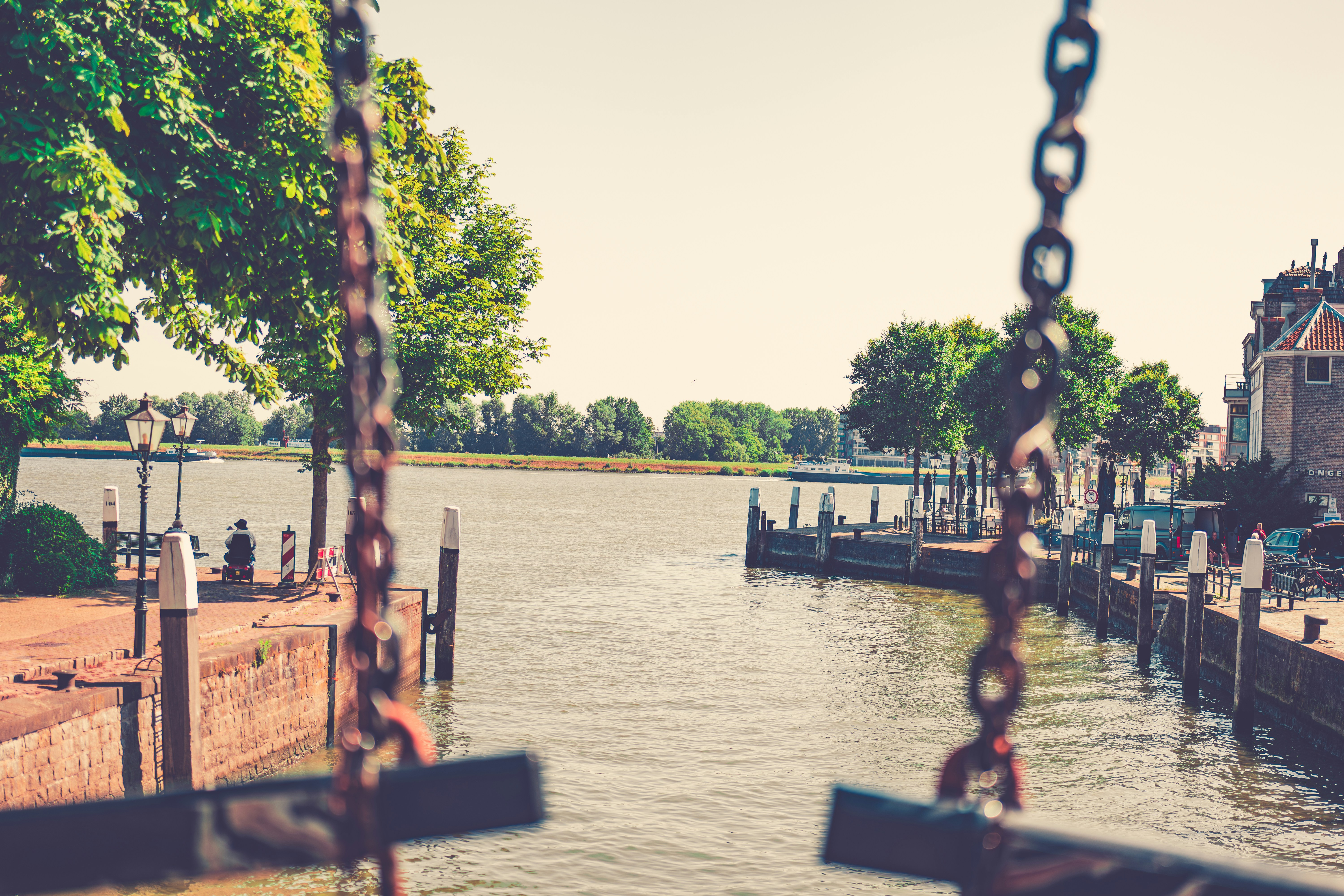 Rusty chains frame a tranquil canal with trees and buildings.