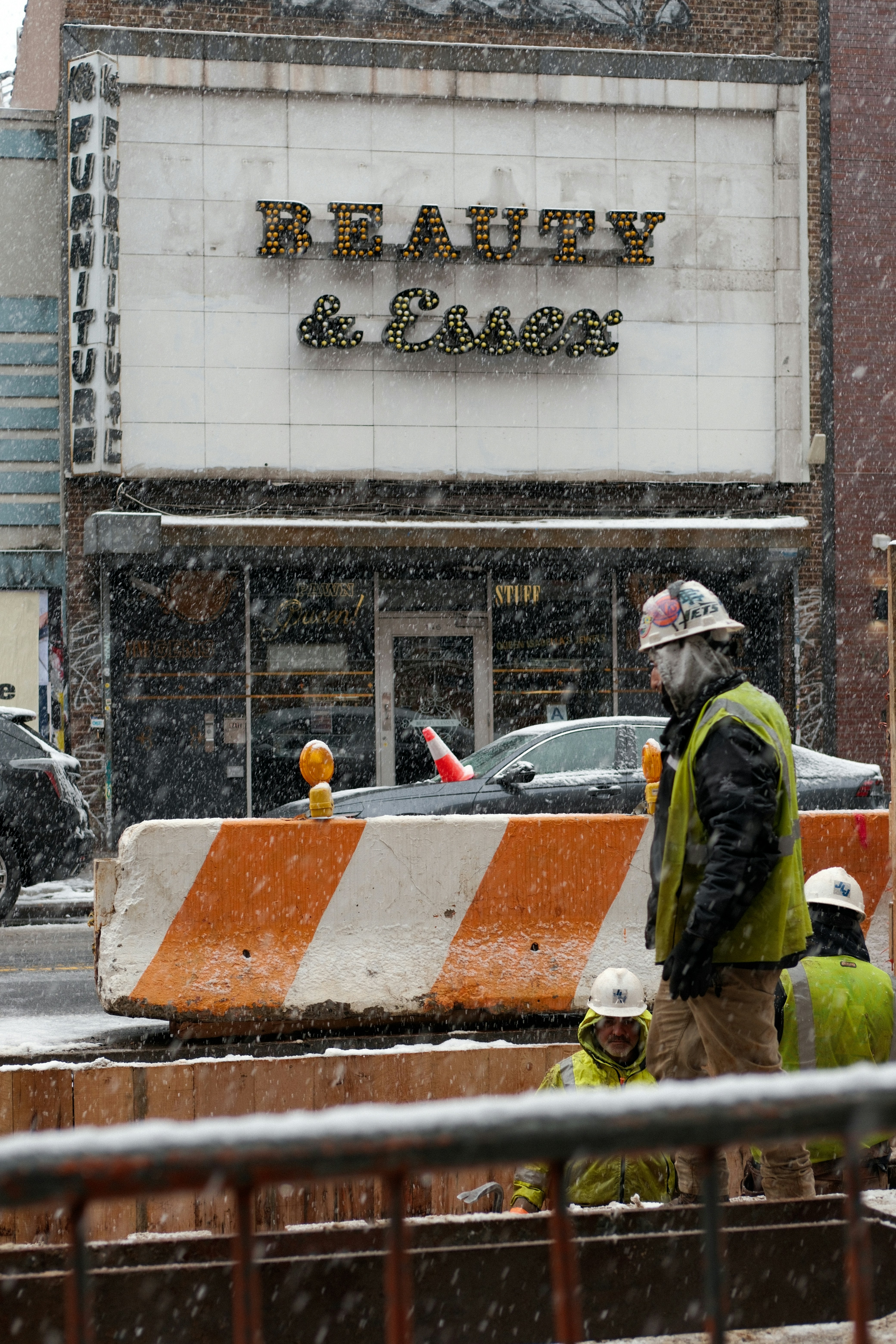 Snow-Soaked storefront target: safety barriers and workers against a Beauty & Essex marquee