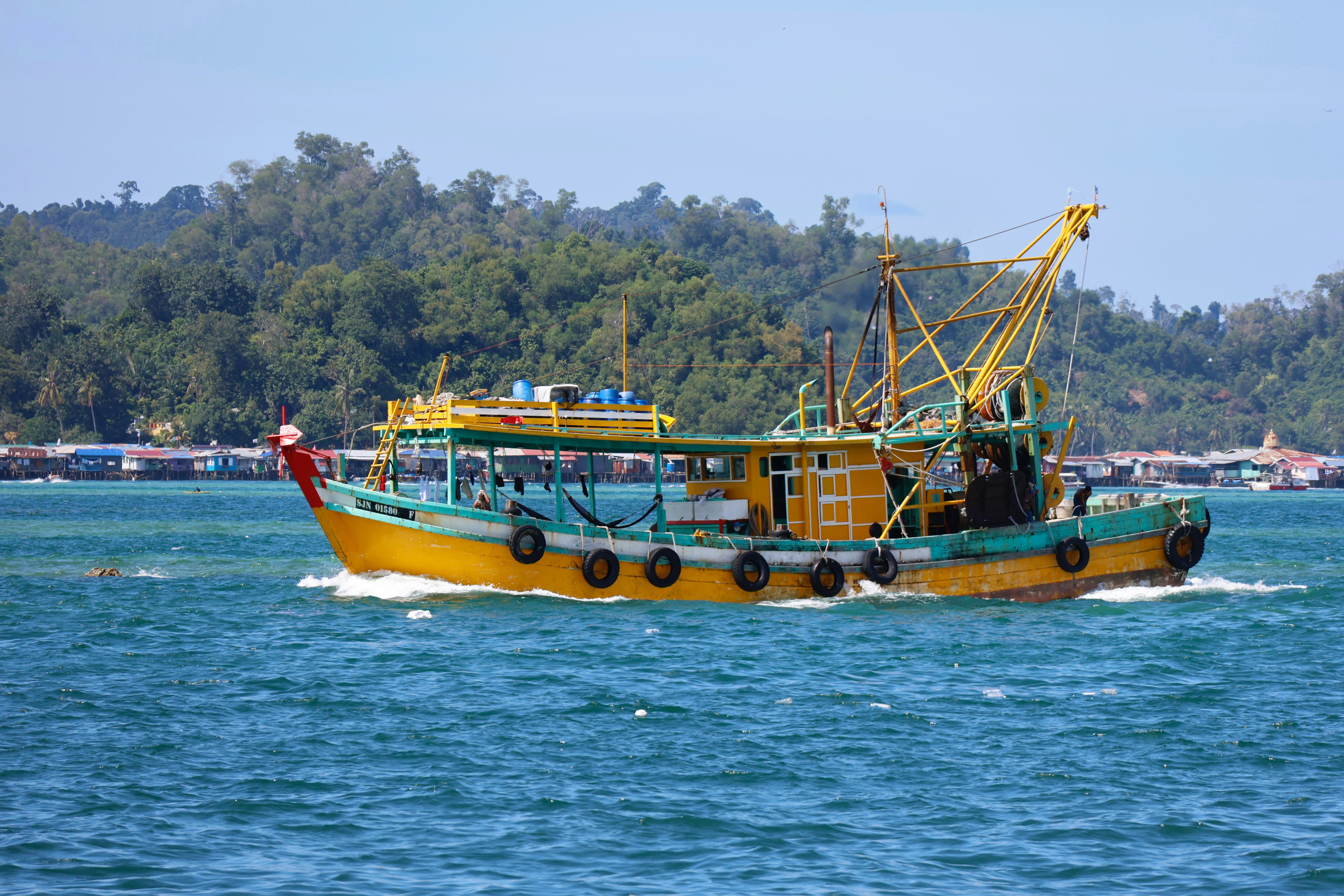 Yellow fishing boat slicing through blue-green sea with distant coastline