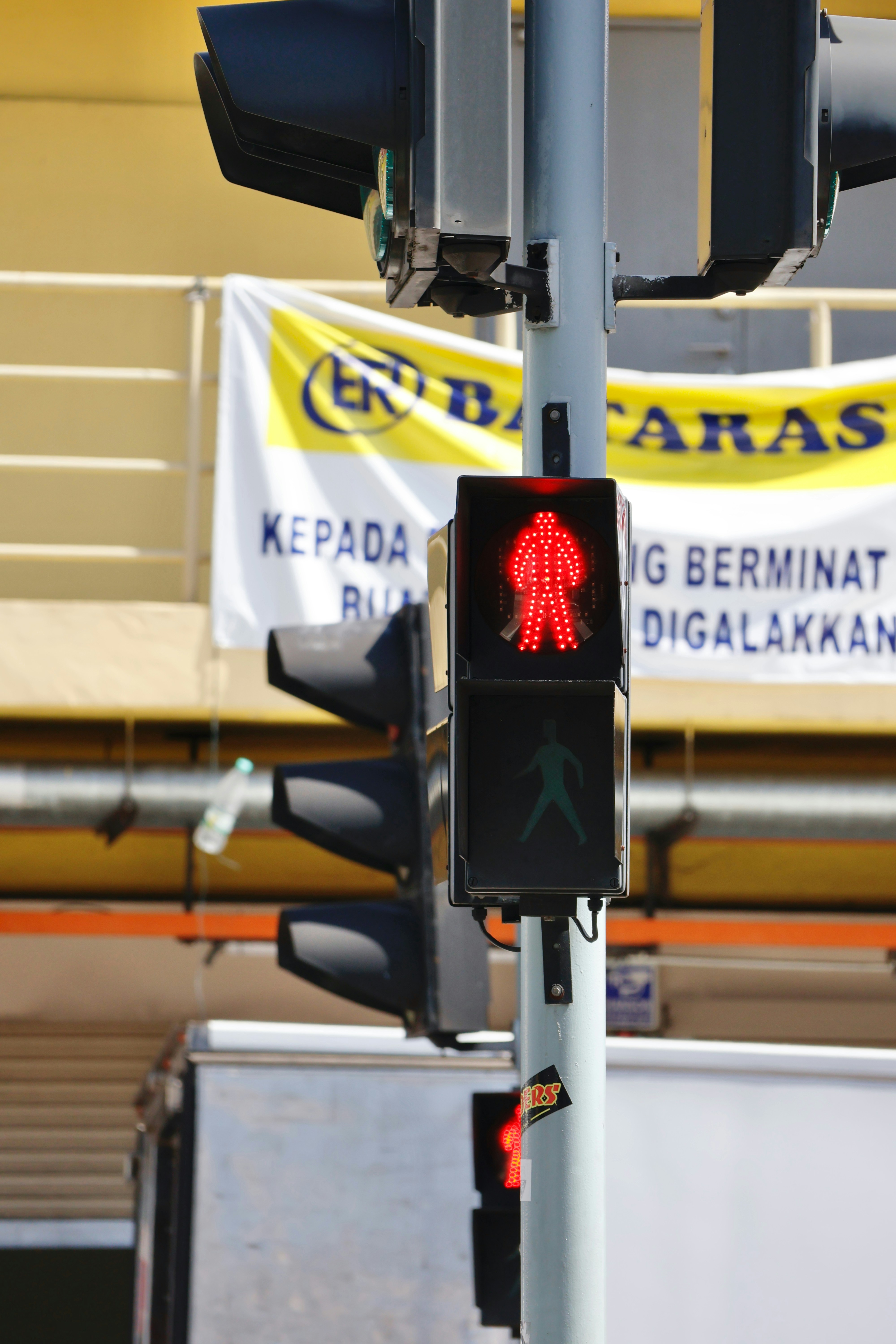 Red Pedestrian Signal Illuminates Urban Crosswalk Under Yellow-Backdrop Banner