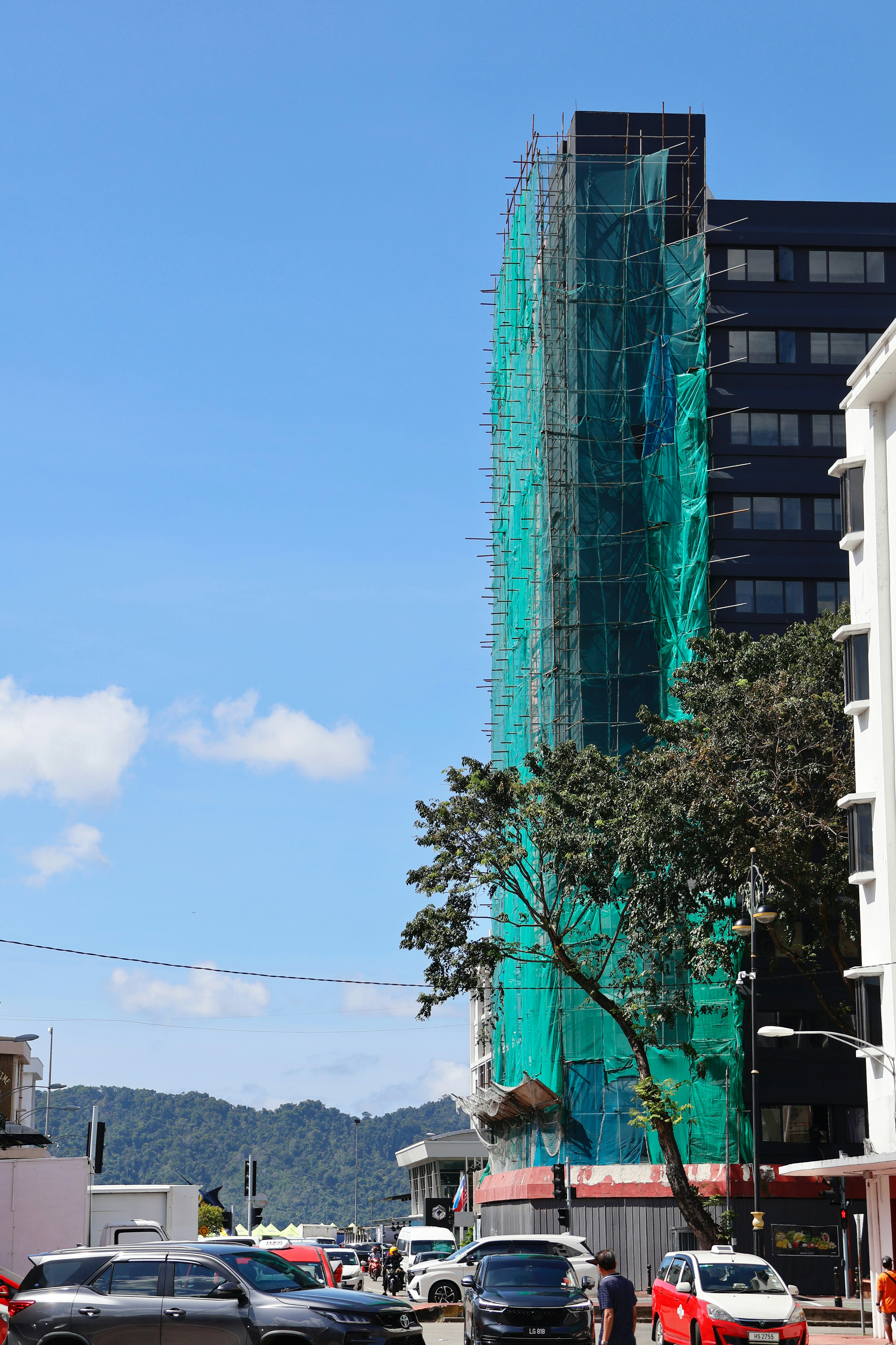 Under Construction Veil: a Tower Clad in Green Netting Rises Over a Busier Street