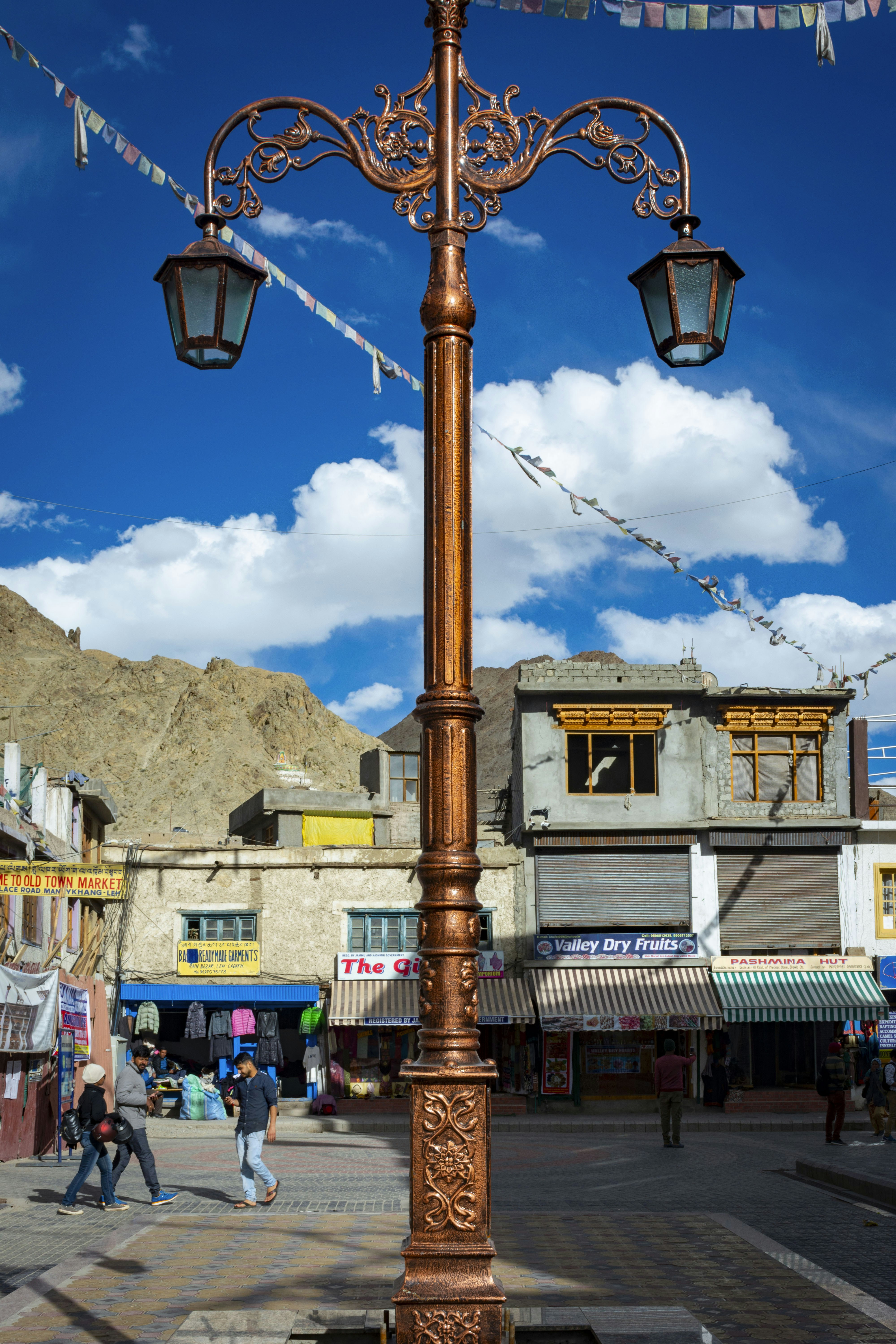 Ornate Street Lamp Framing a Bustling Market Against Tibetan Highlands