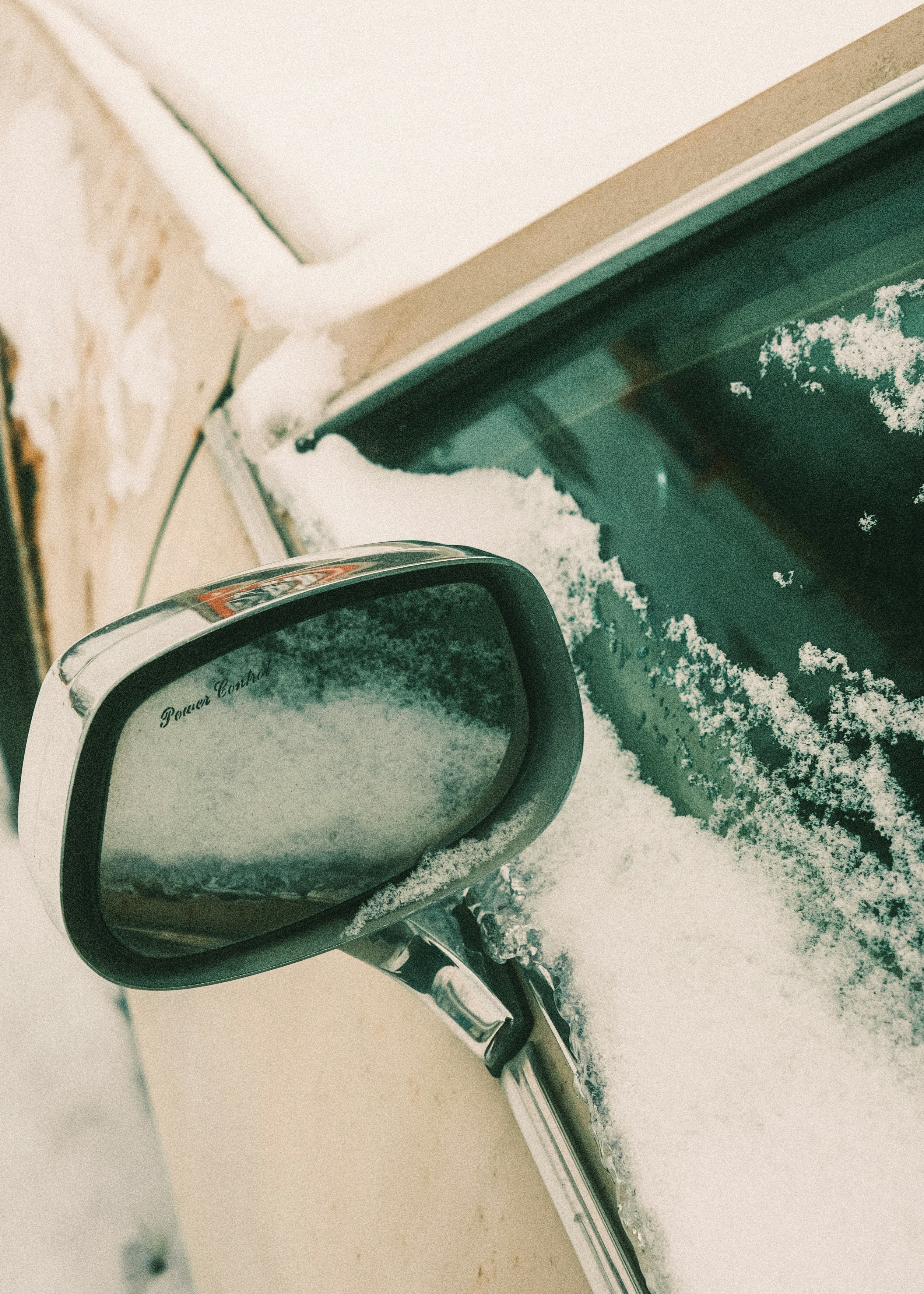Icebound Mirror: A Snow-Dusted Side View of a Car Exterior