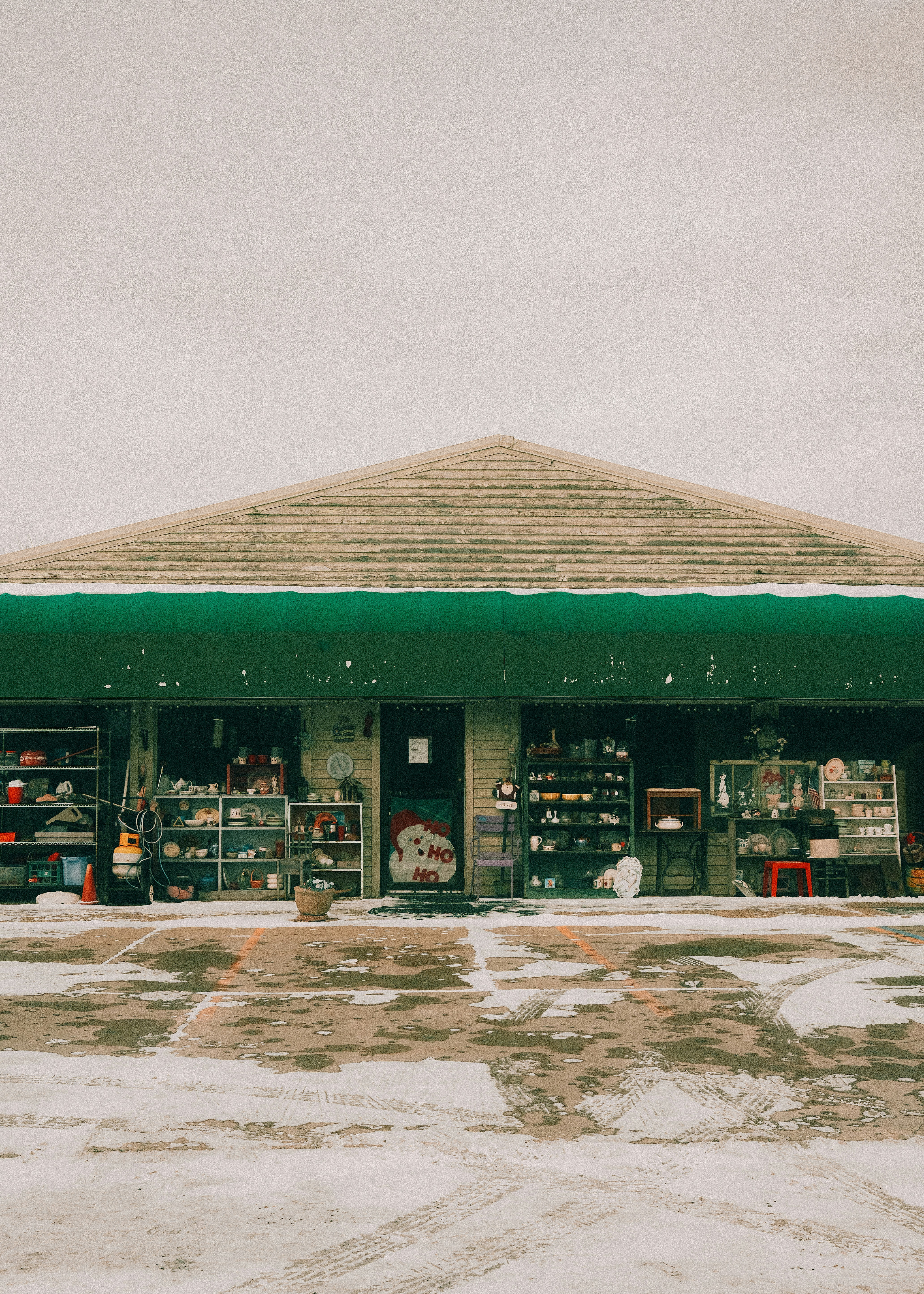 Green-roofed shopfront with outdoor goods display on a snowy lot