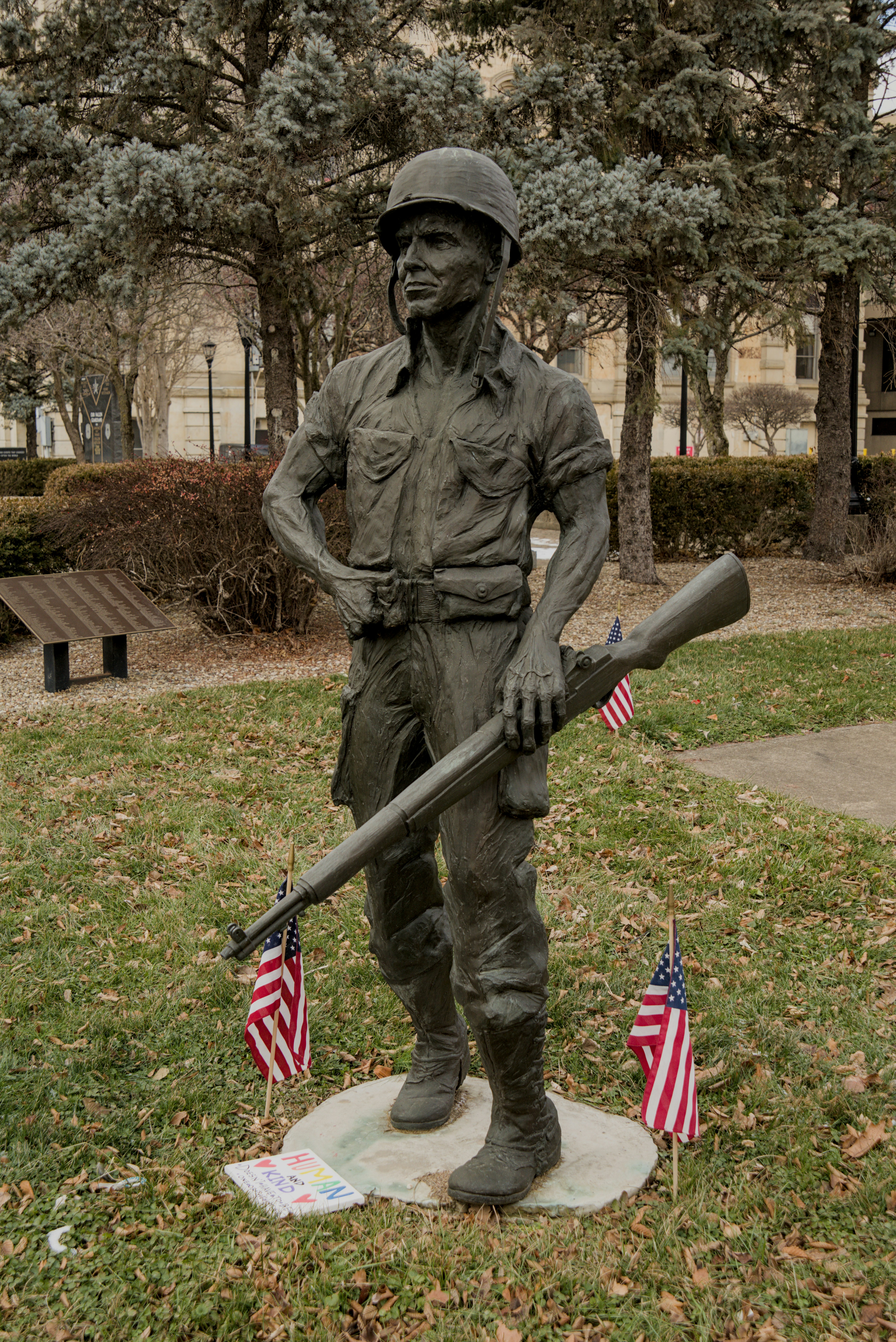 Brass Sentinel: A Soldier Statue with Rifle amidst Memorial Flags