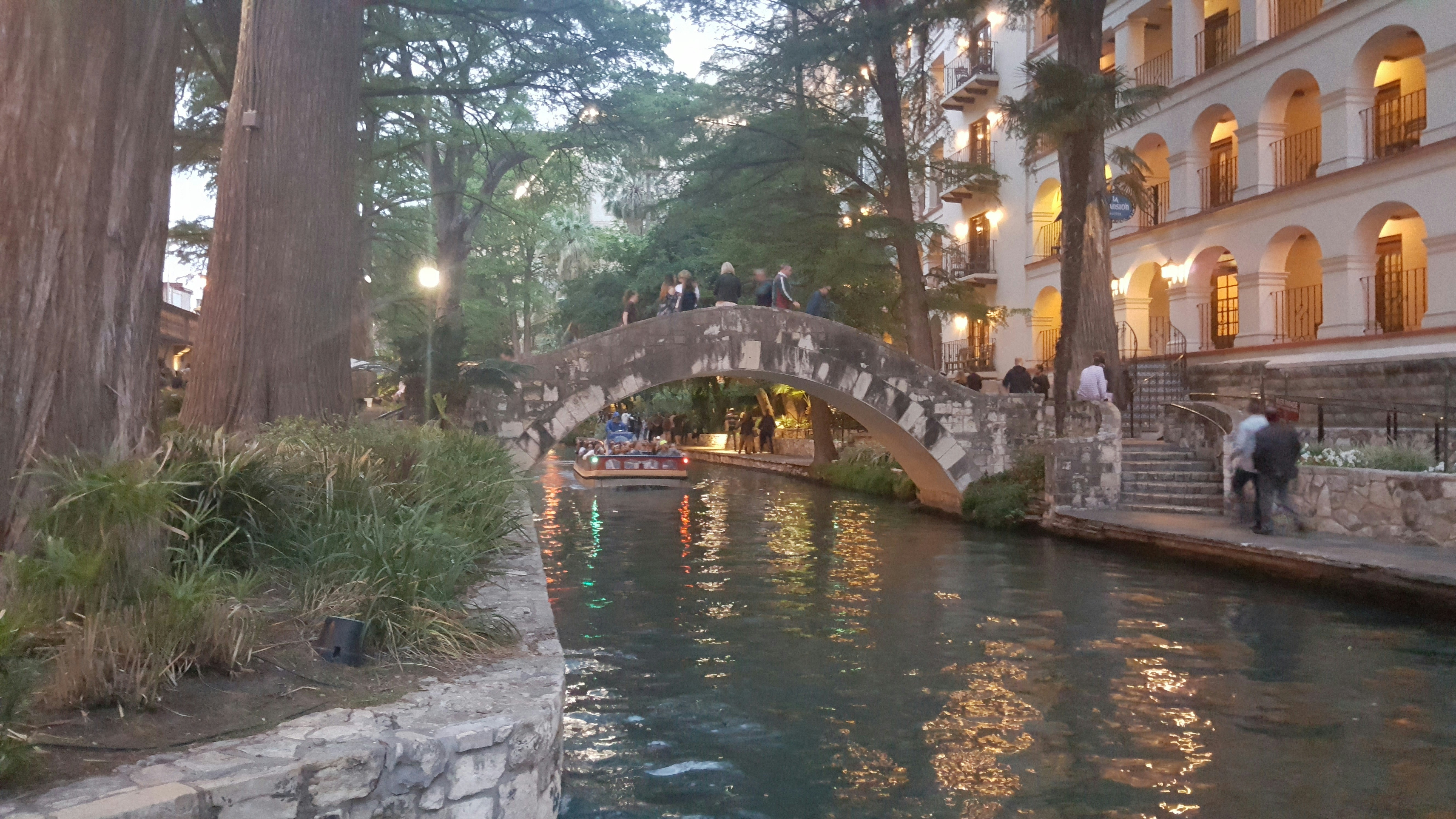 Stone-arched pedestrian bridge over a tranquil canal at dusk