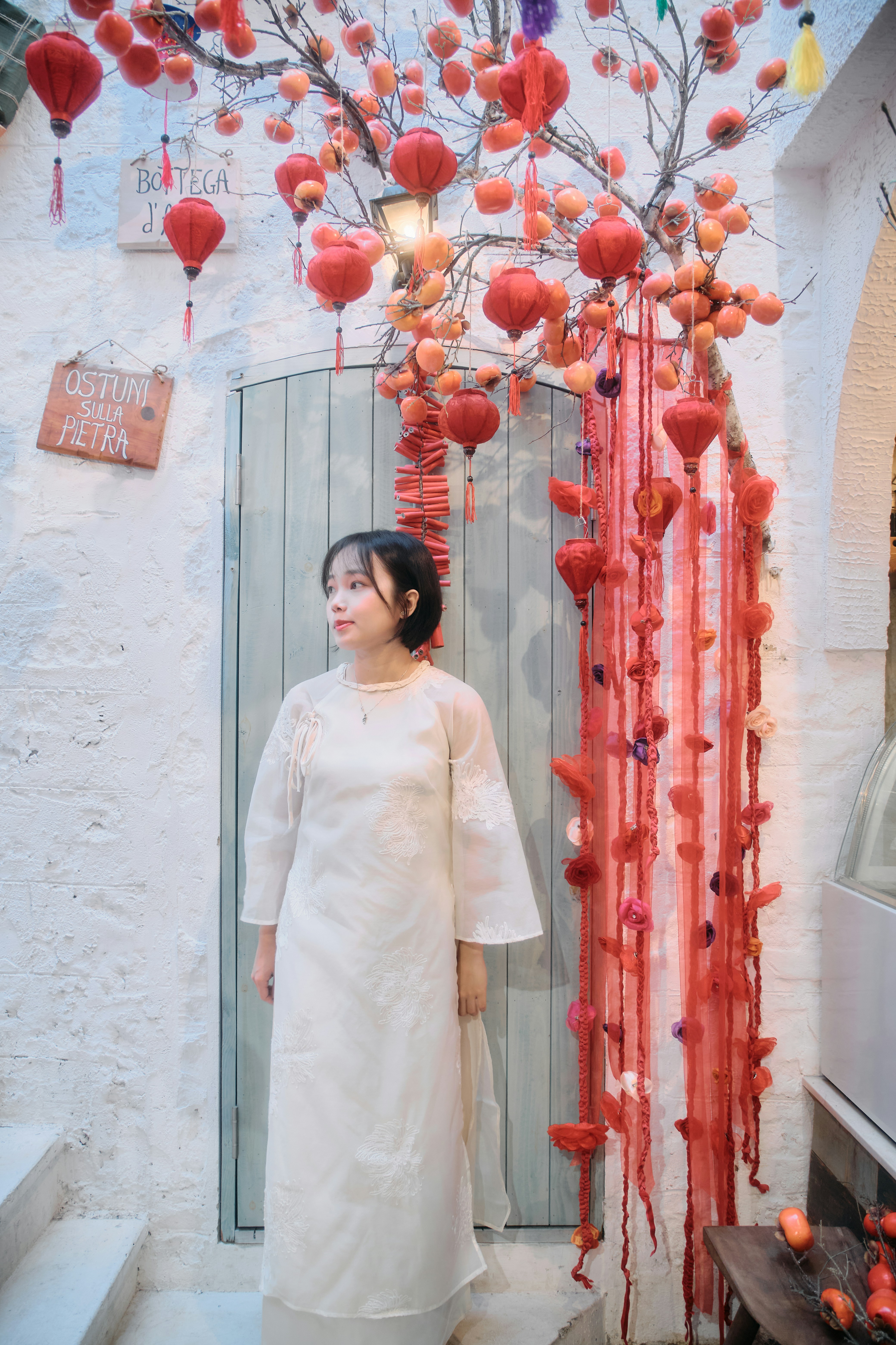 Portrait beneath a Crimson Garden: a woman in white amid hanging lanterns
