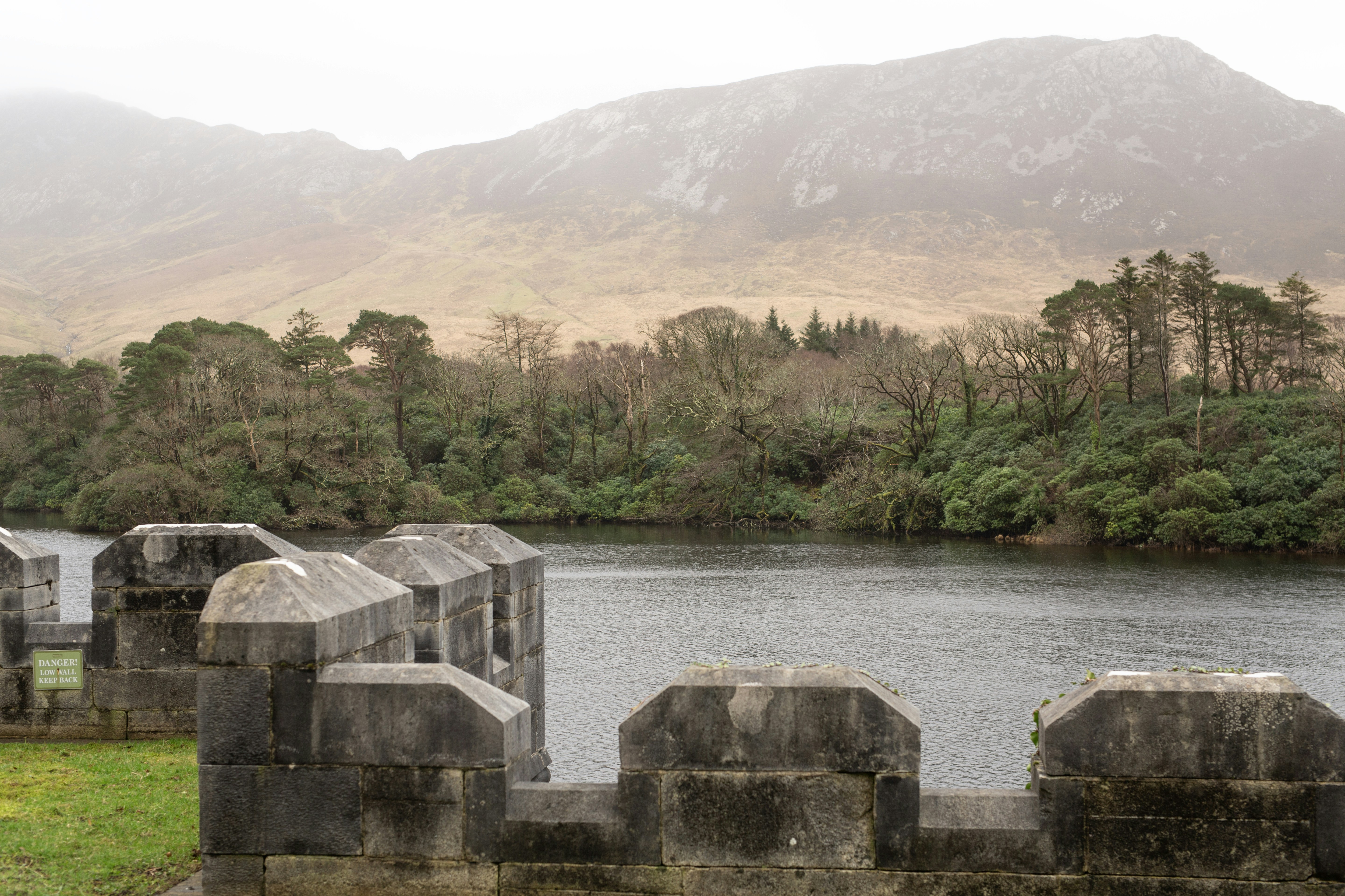 Stone bastions along a calm lakeshore with a backdrop of trees and distant mountains, framed by a low-horizon composition. An outdoor landscape scene showing historic masonry and natural scenery.