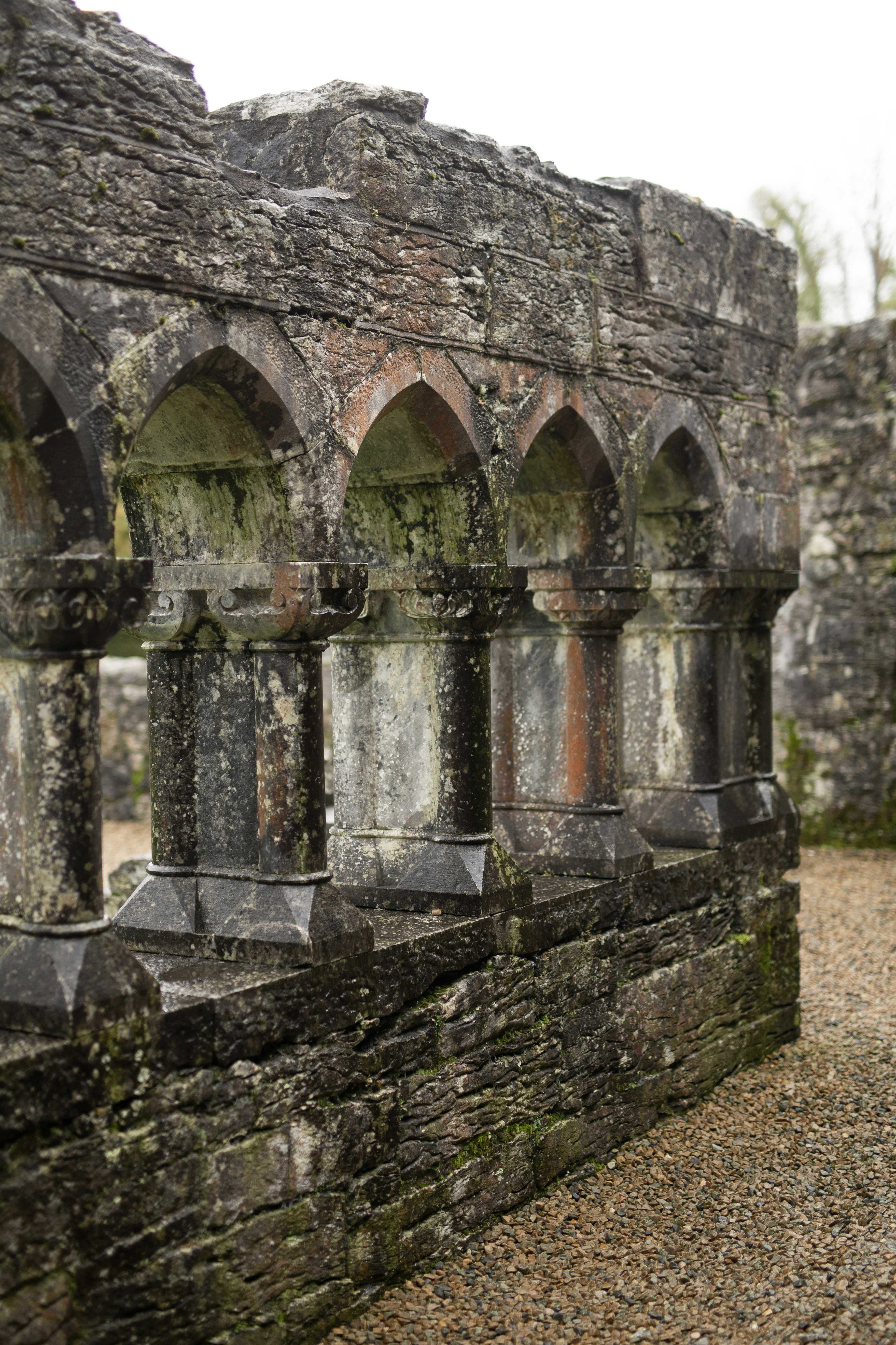 Mossy Gothic Arcade: Weathered Stone Arches Along a Pebble Walk