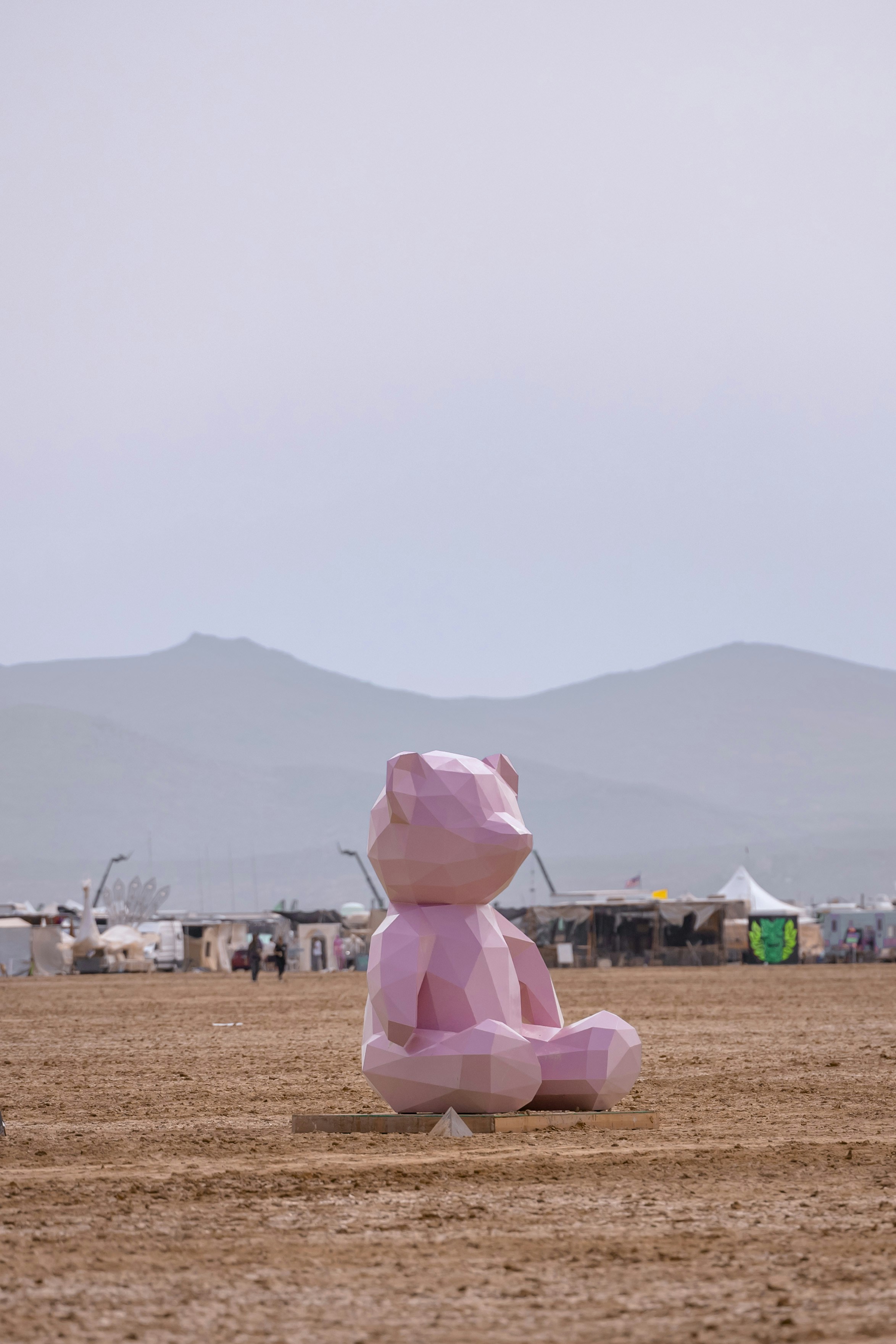 Geometric Pink Bear: A solitary sculpture against a dusty festival backdrop