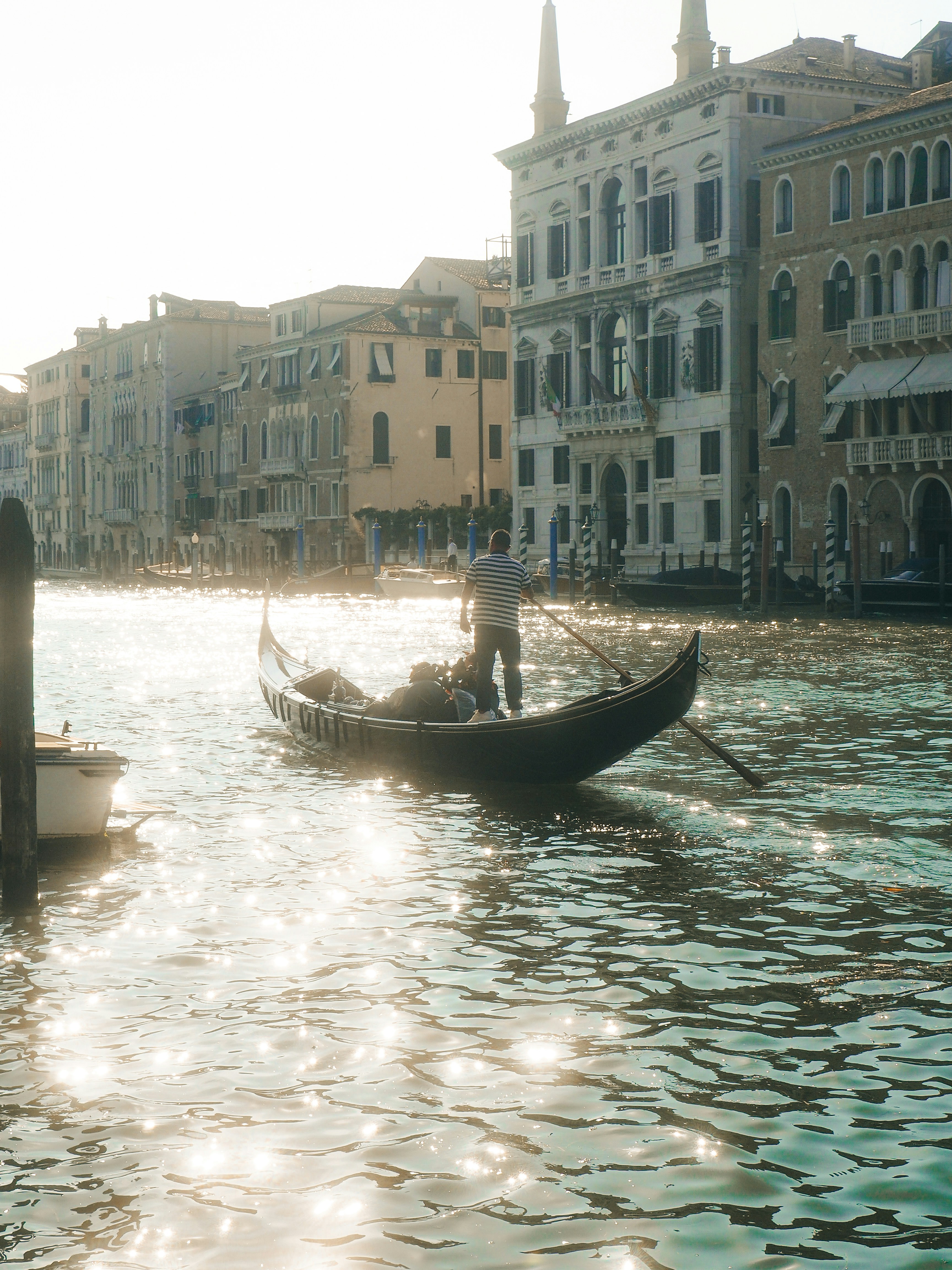 Un gondolero dirige el barco por un canal iluminado por el sol en ...